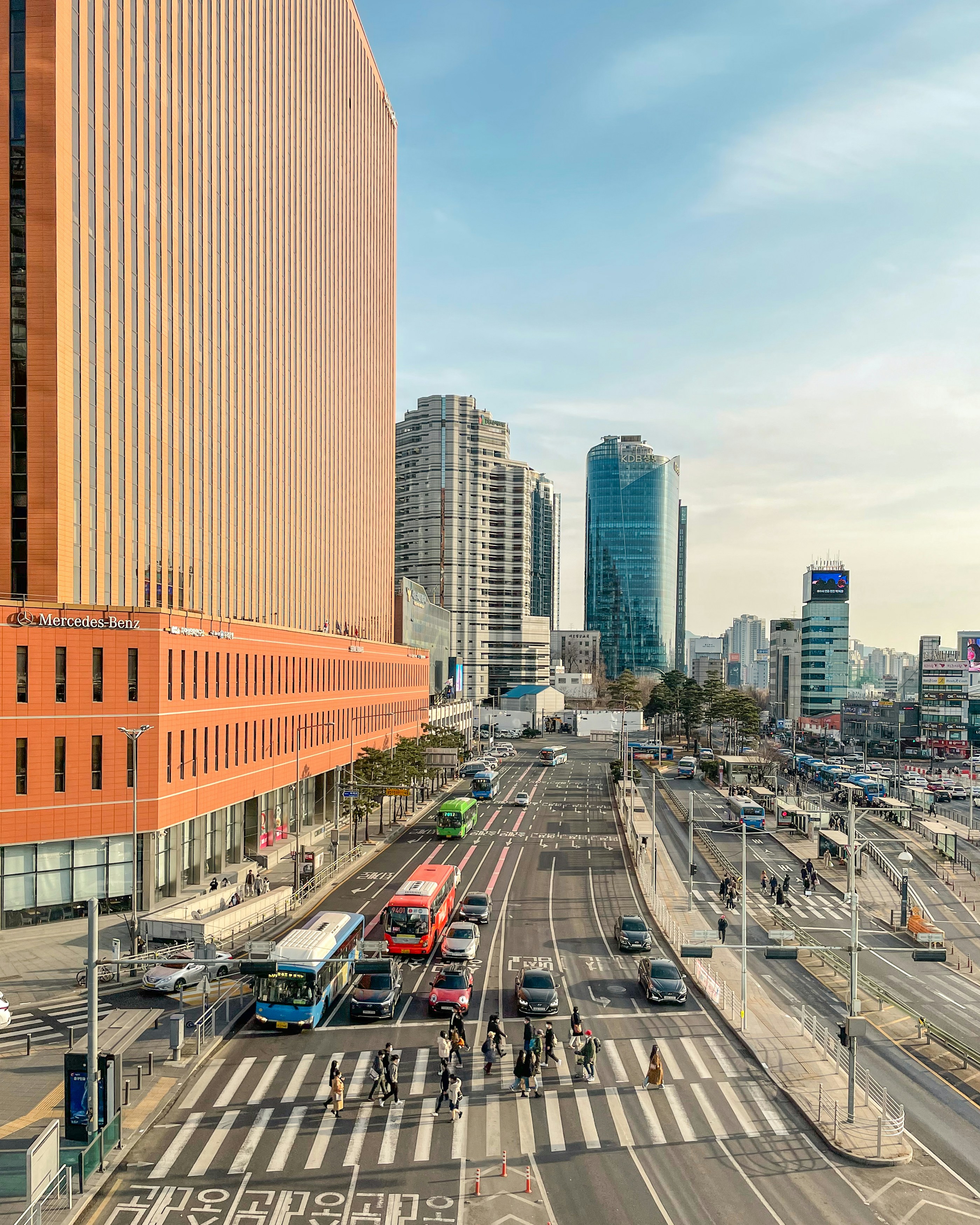 A bustling city intersection showcasing modern skyscrapers and vibrant traffic, with pedestrians navigating the crosswalk. The scene captures the essence of urban life.