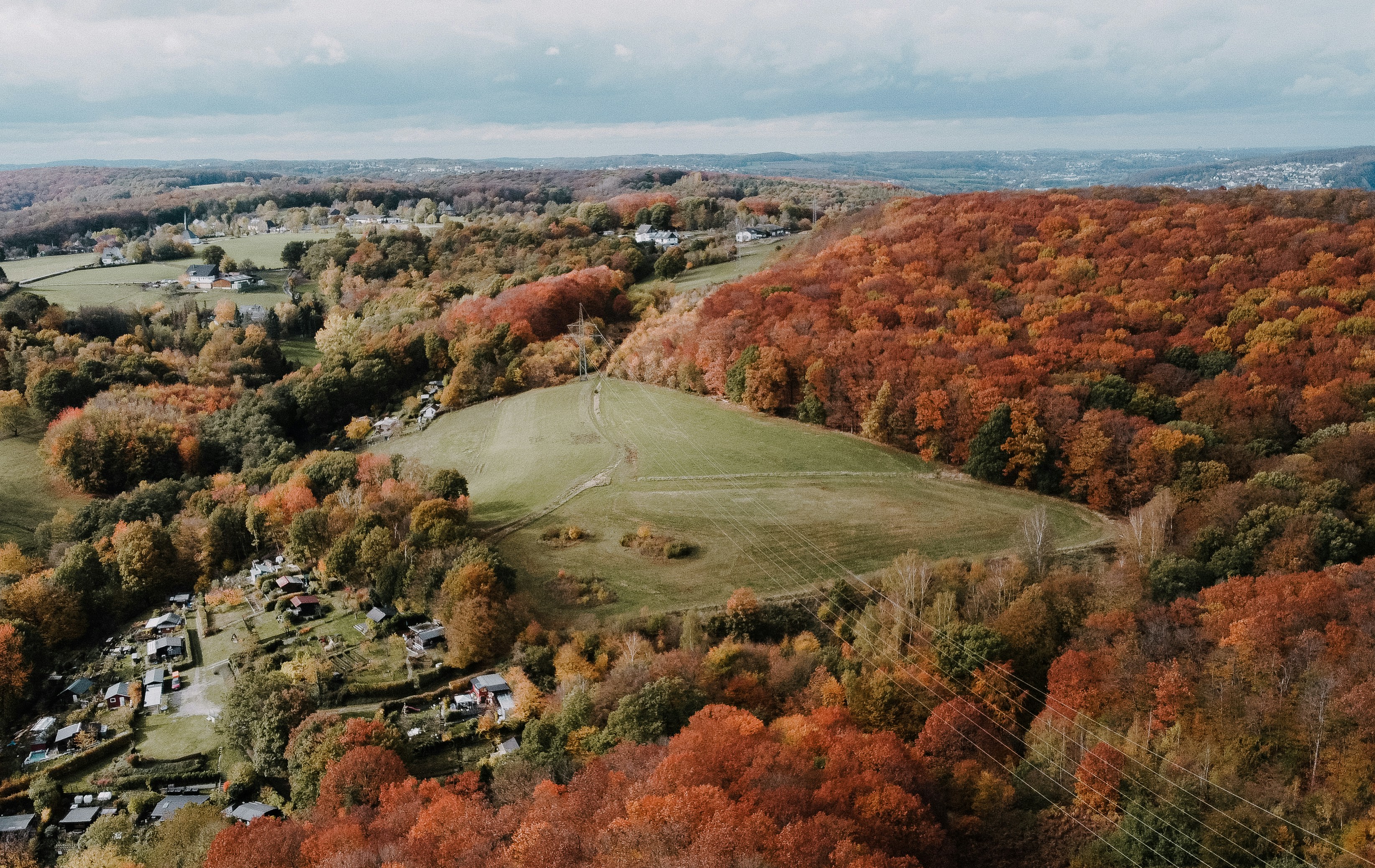Vibrant autumn foliage blankets the landscape, revealing a serene field bordered by colorful trees. The aerial view captures the essence of the season's transformation.