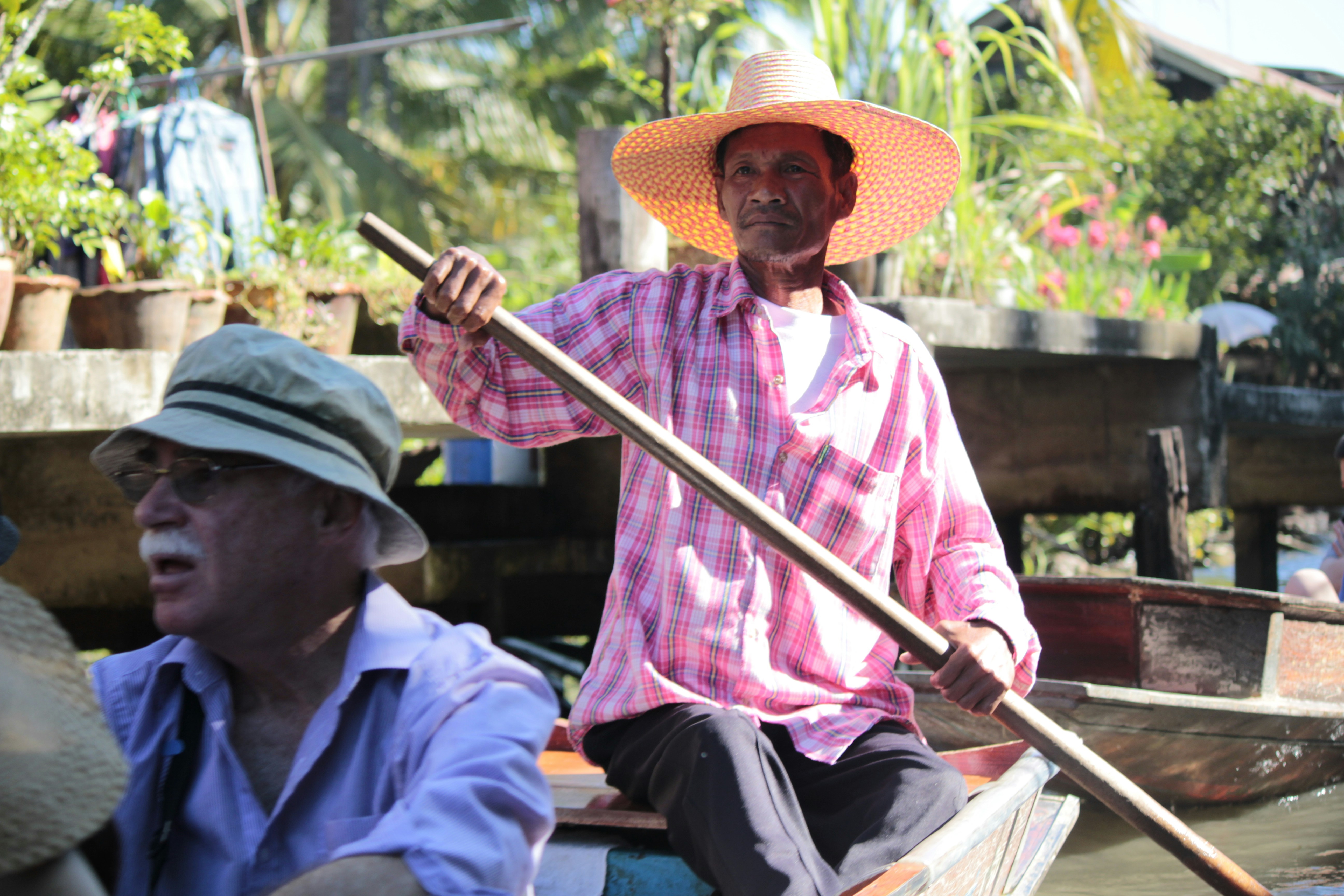 A man in a wide-brimmed hat rows a wooden boat through a vibrant canal, showcasing the essence of local trade and culture.