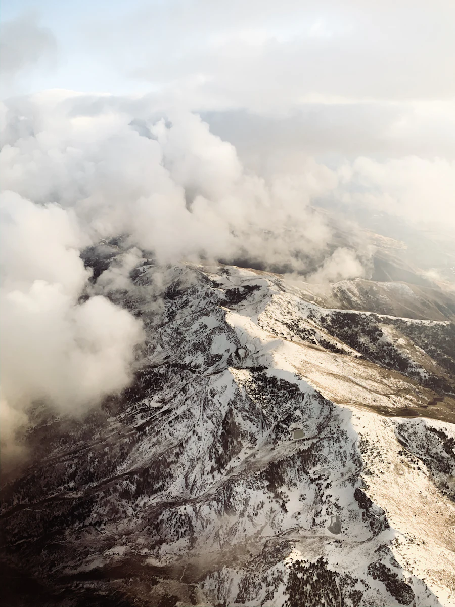 Snow-dusted ridge carved by clouds, viewed from above in daylight. Aerial landscape photograph of rugged peaks.
