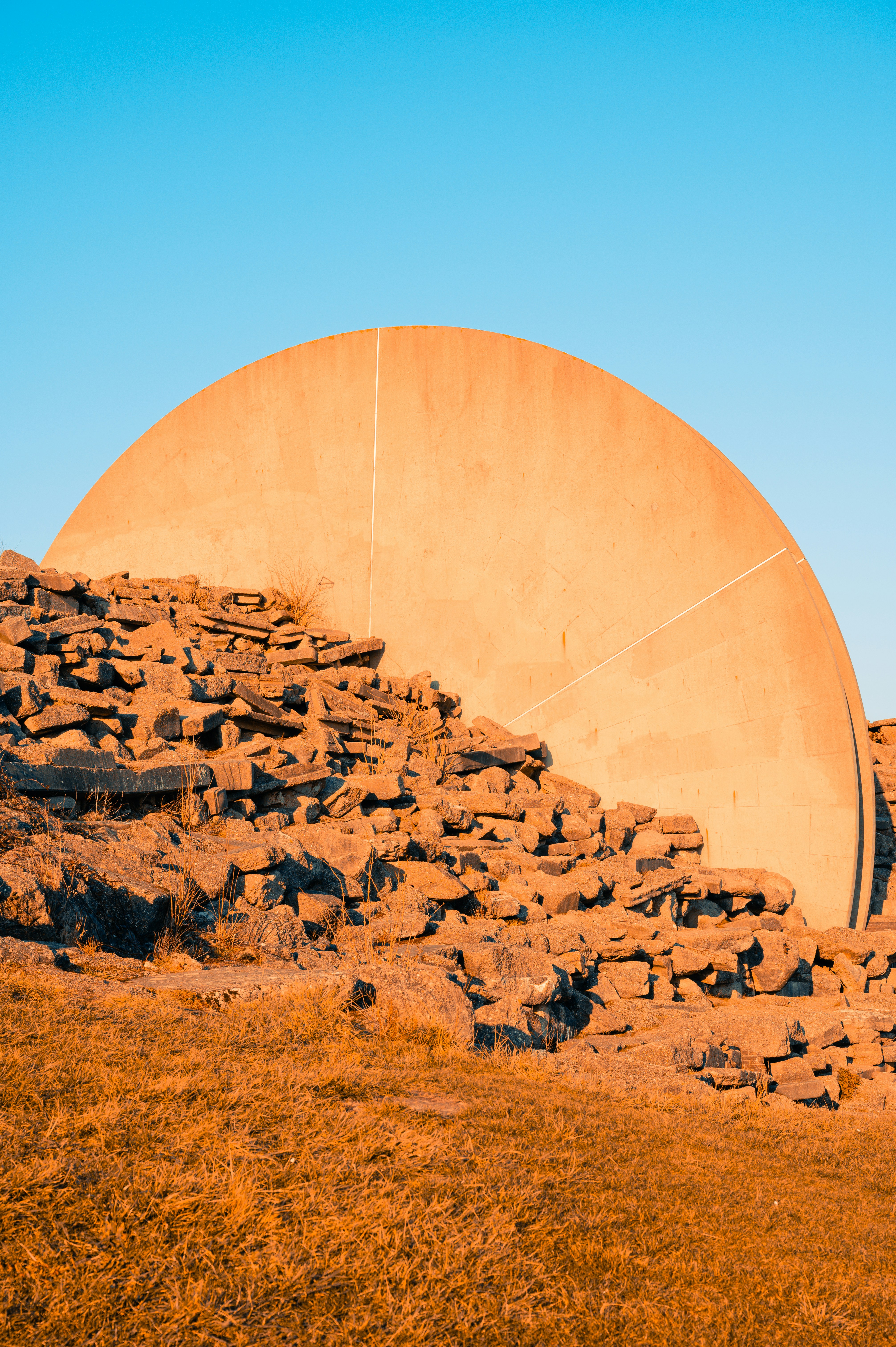 Sunlit Sentinel: A Circular Radar Dish Rising from Rubble Under a Clear Blue Sky