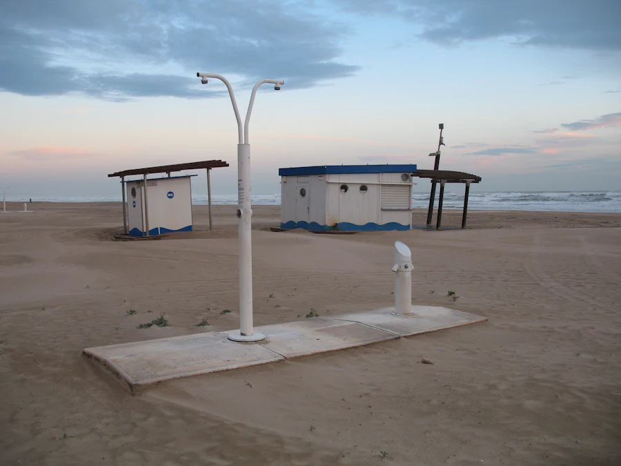Small beach service buildings and lamp posts sit on a sandy shore under a pastel evening sky, with the ocean in the background.