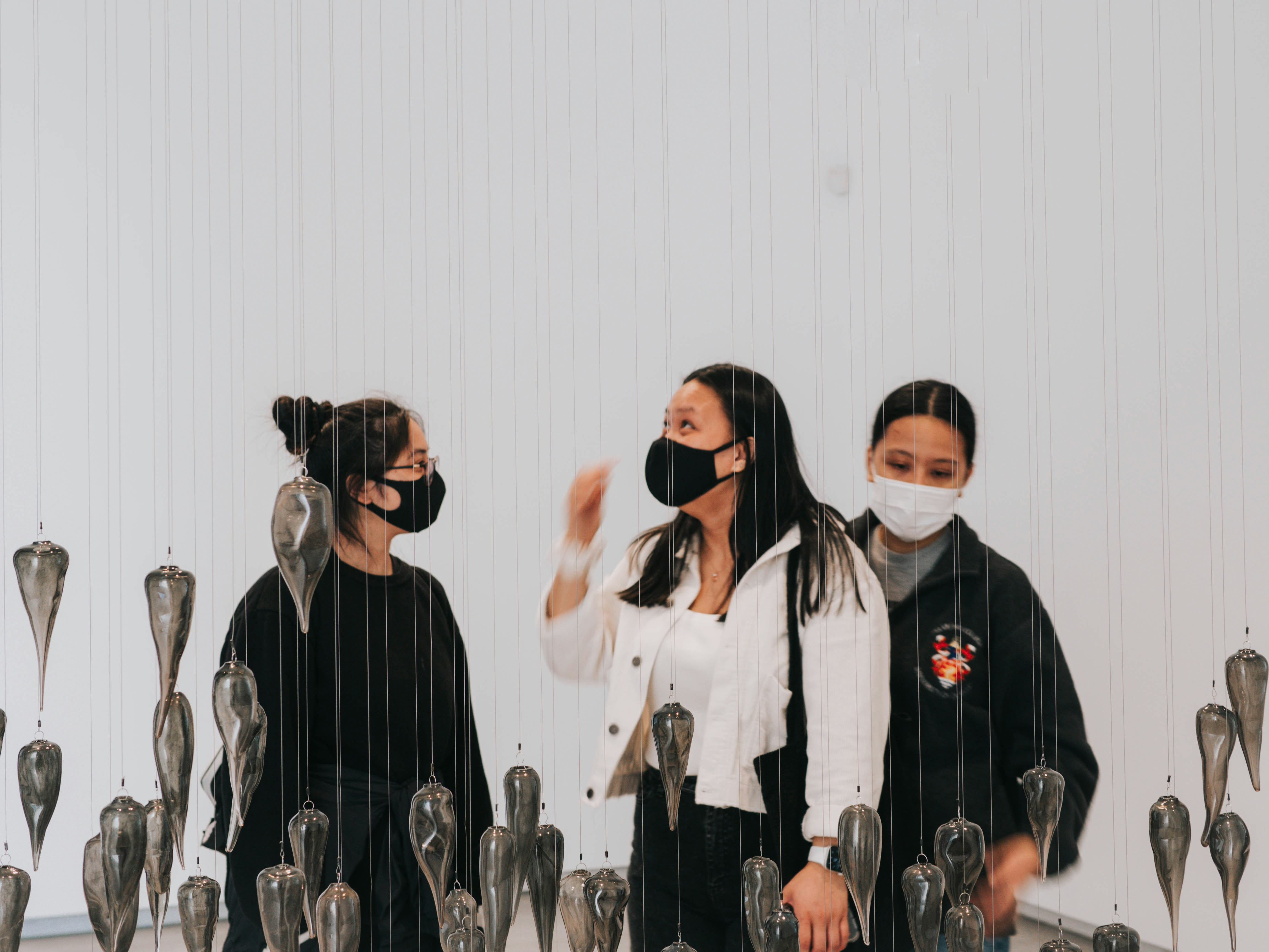 Three Masked Figures Amid a Forest of Metal Teardrops