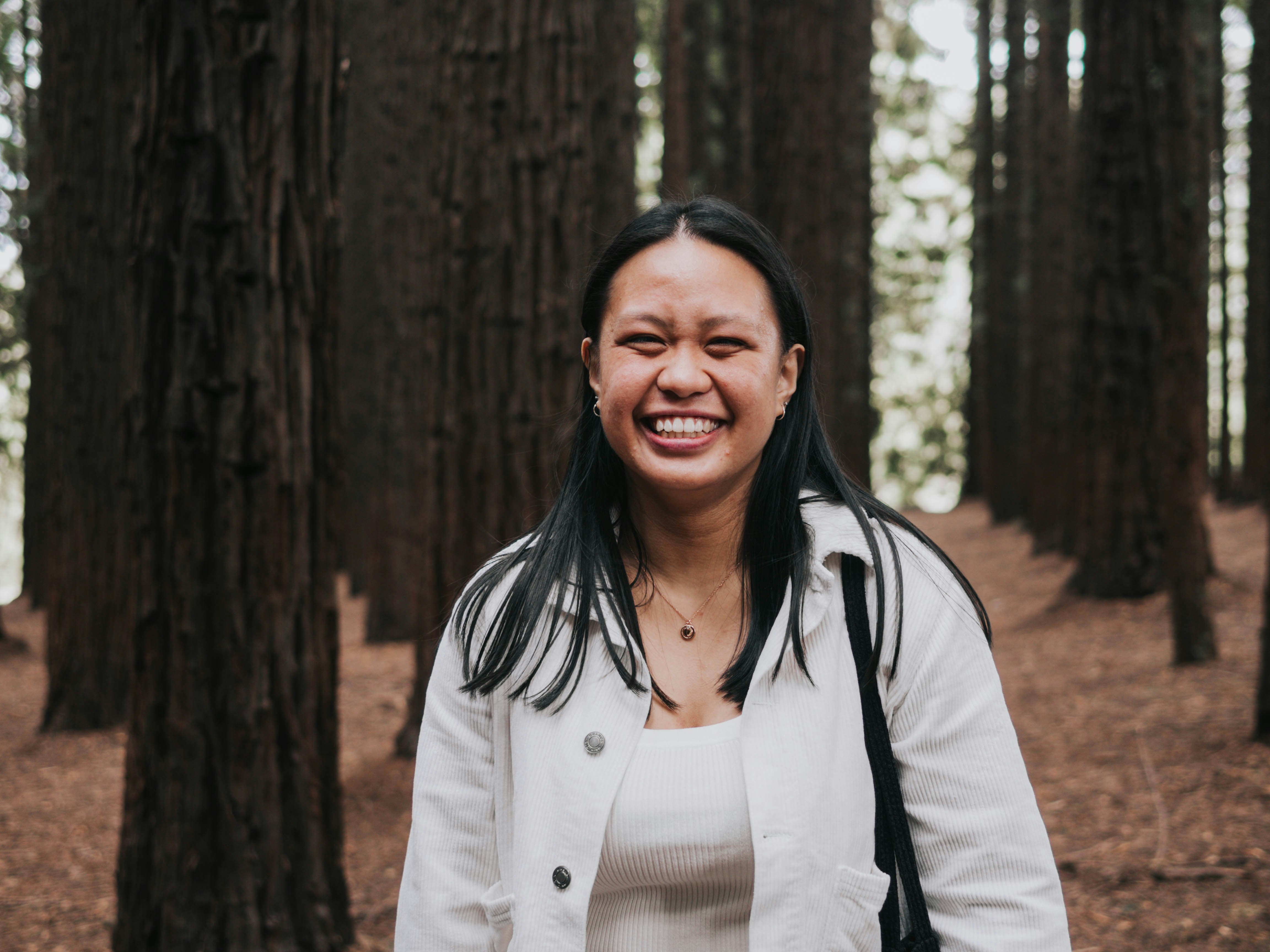 Person smiling broadly among tall trees in a serene forest.