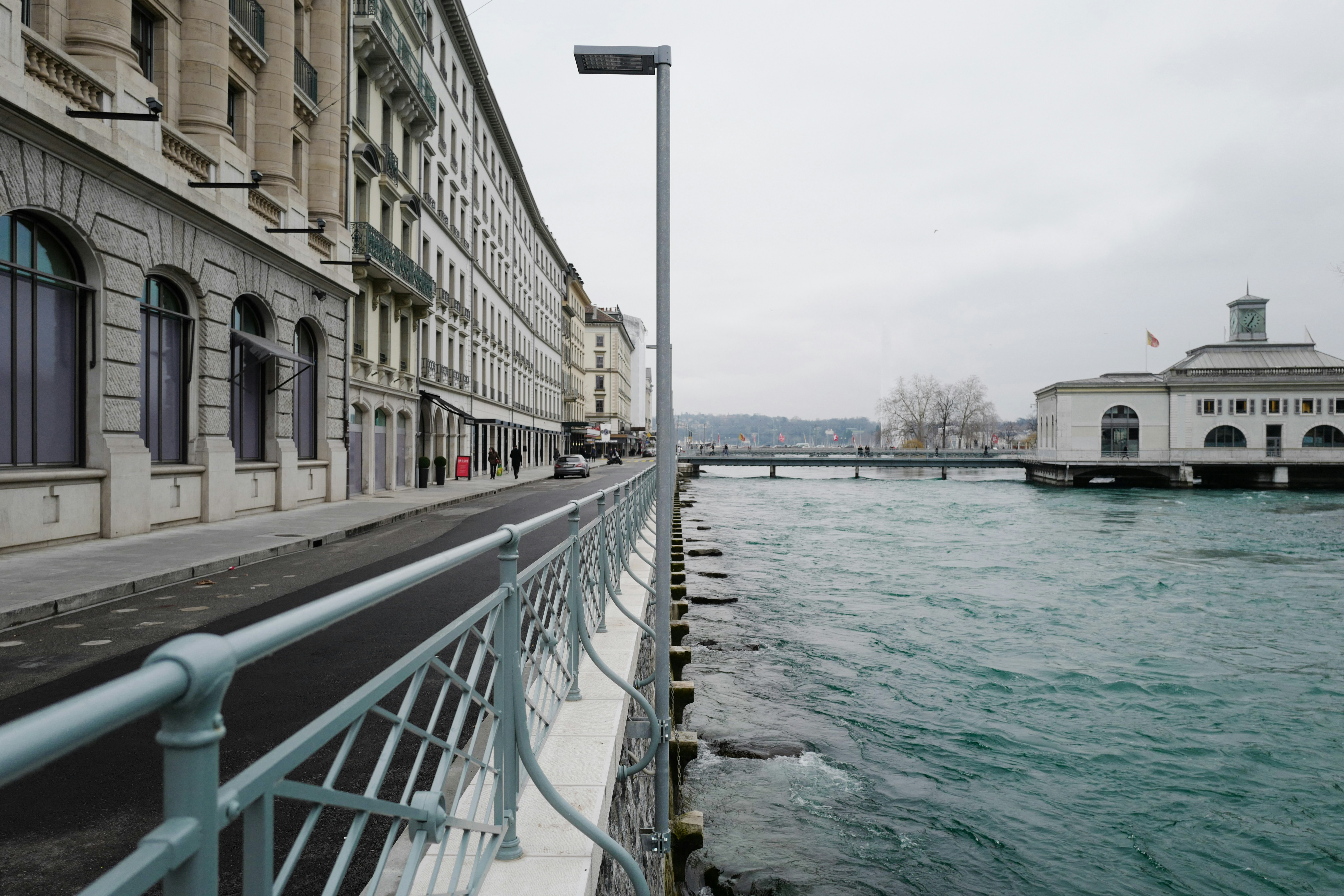 A tranquil riverside scene featuring a modern building alongside a flowing body of water, with a hint of urban architecture in the background.