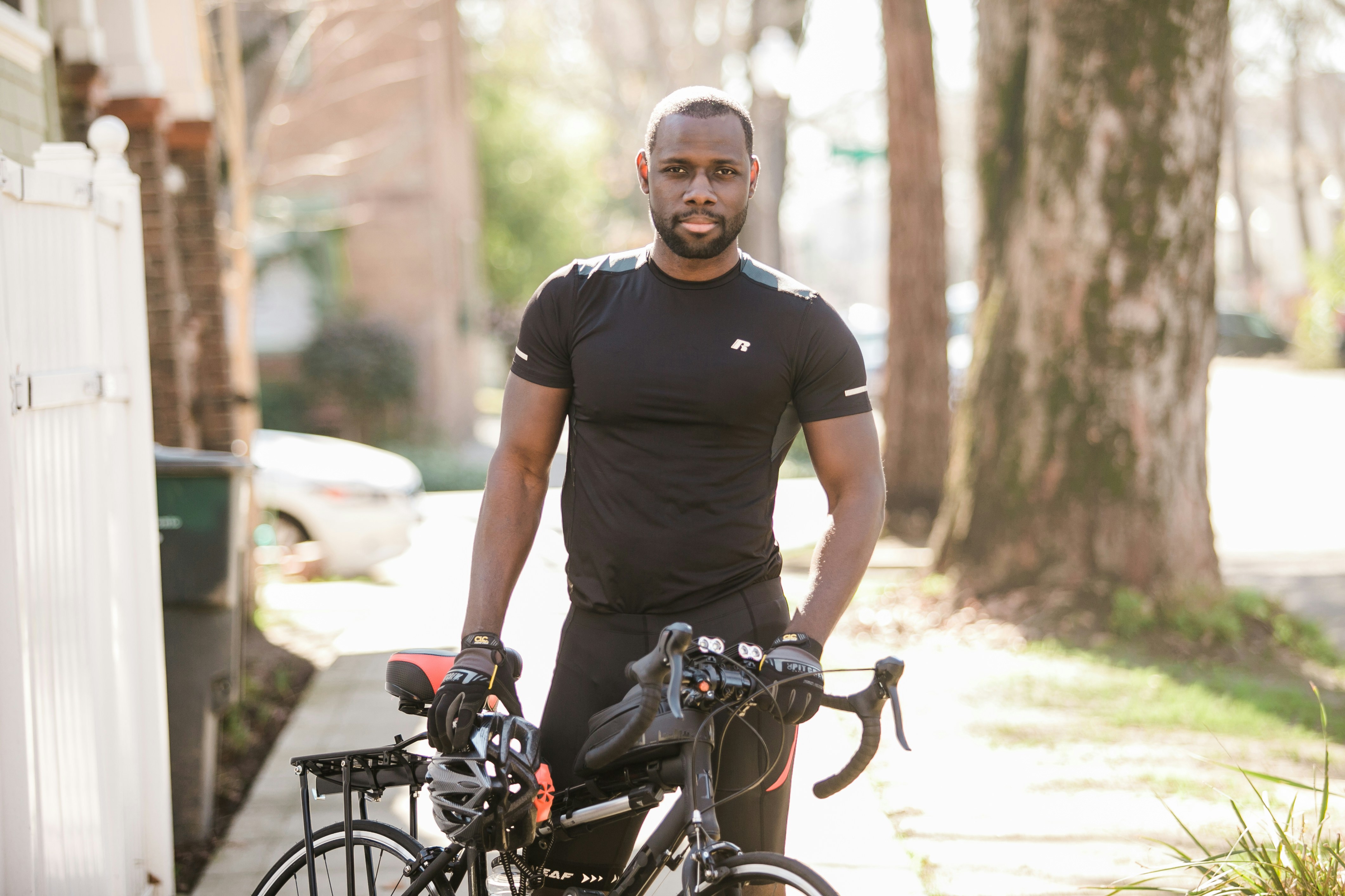 Athlete standing beside a bicycle on a sunlit sidewalk, showcasing a moment of readiness before a ride.