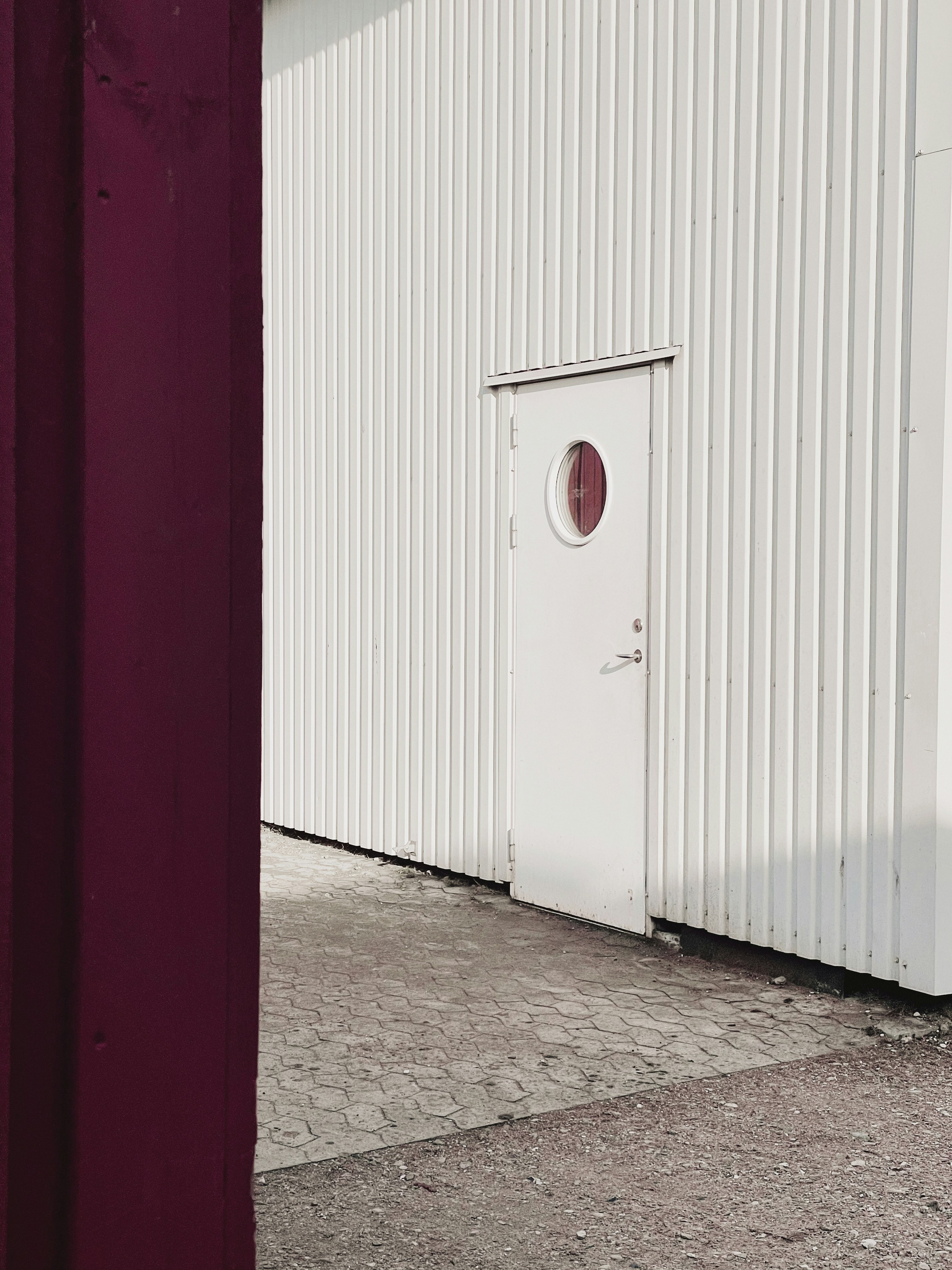 Round Windowed Door on a Quiet White Metal Facade