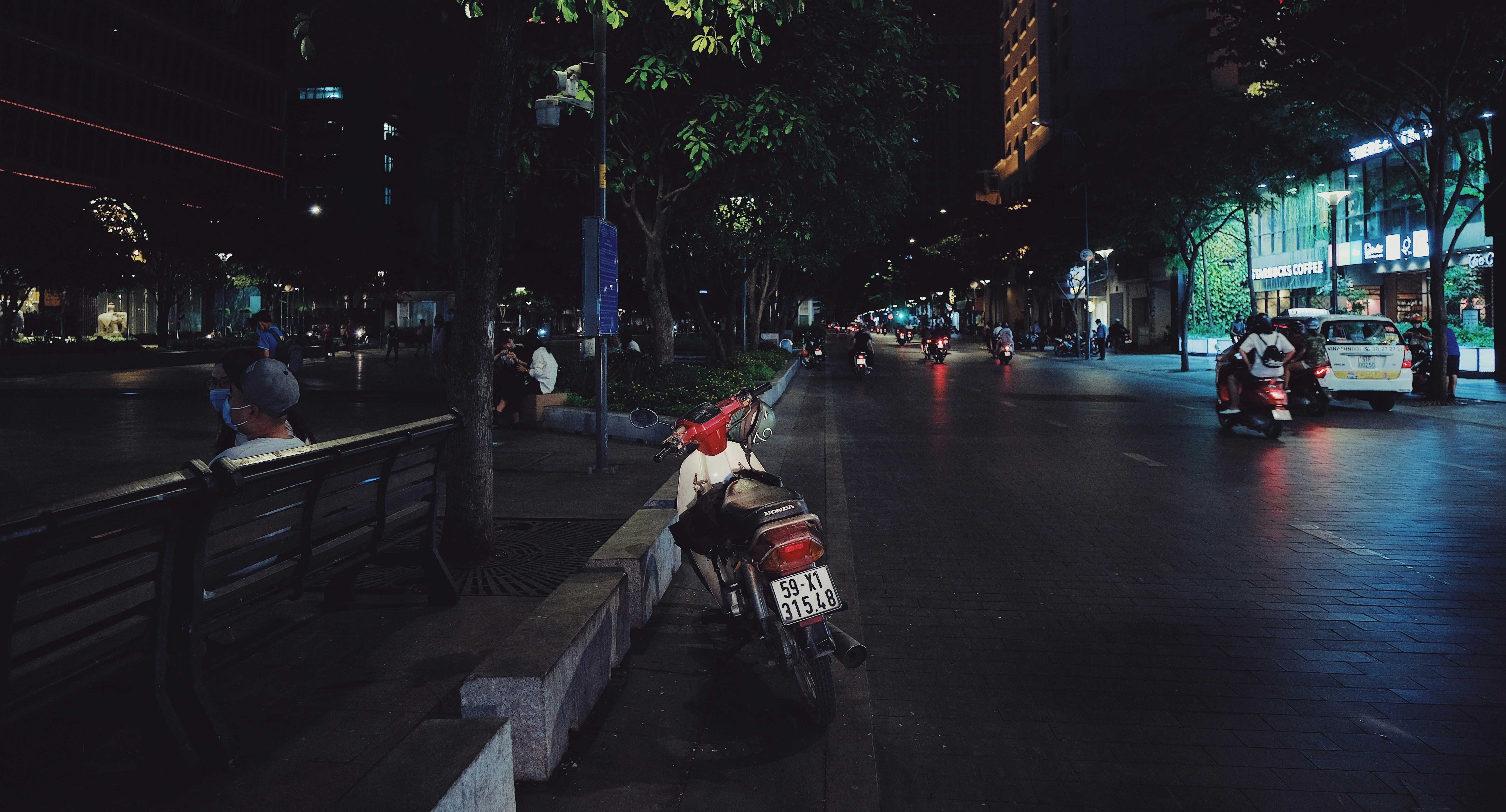 A motorcycle parked on a city street at night, illuminated by vibrant storefronts and streetlights. The scene captures the essence of urban life after dark.
