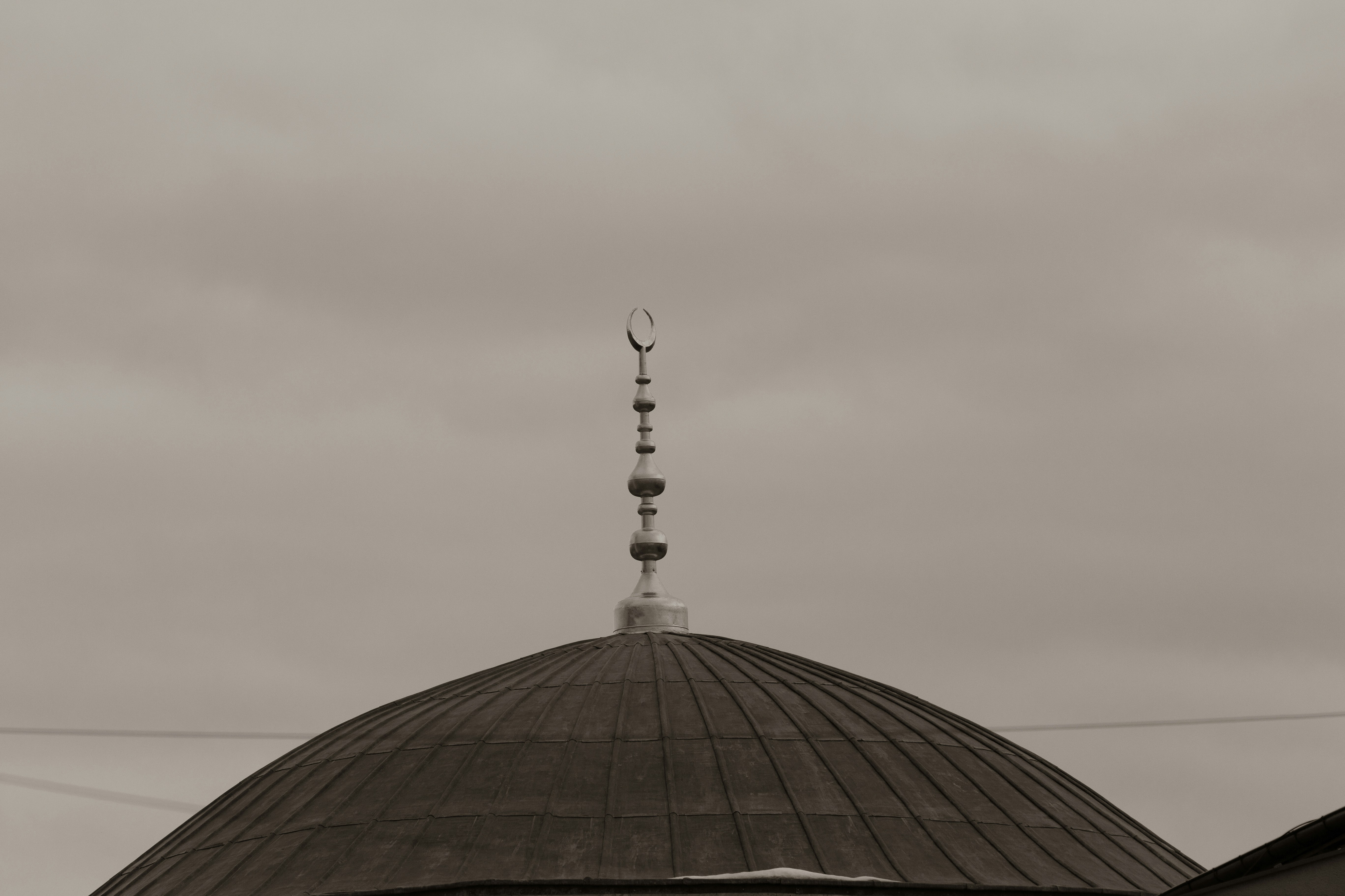 Crescent moon and star atop a mosque dome against a moody sky, symbolizing faith and heritage.