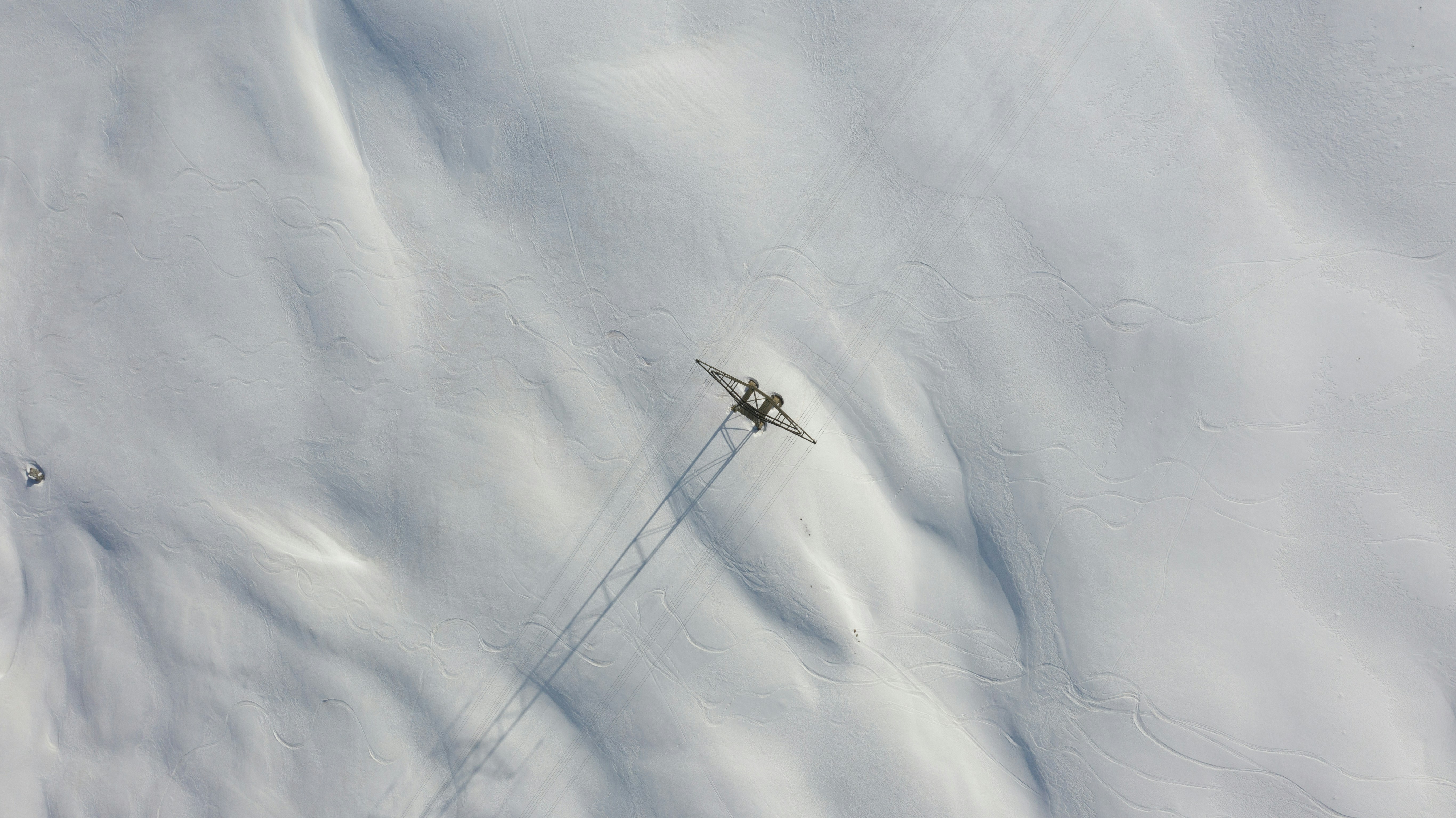 A solitary aircraft casts a long shadow over a vast, undulating blanket of snow, illustrating the stark contrast between man-made and natural elements.