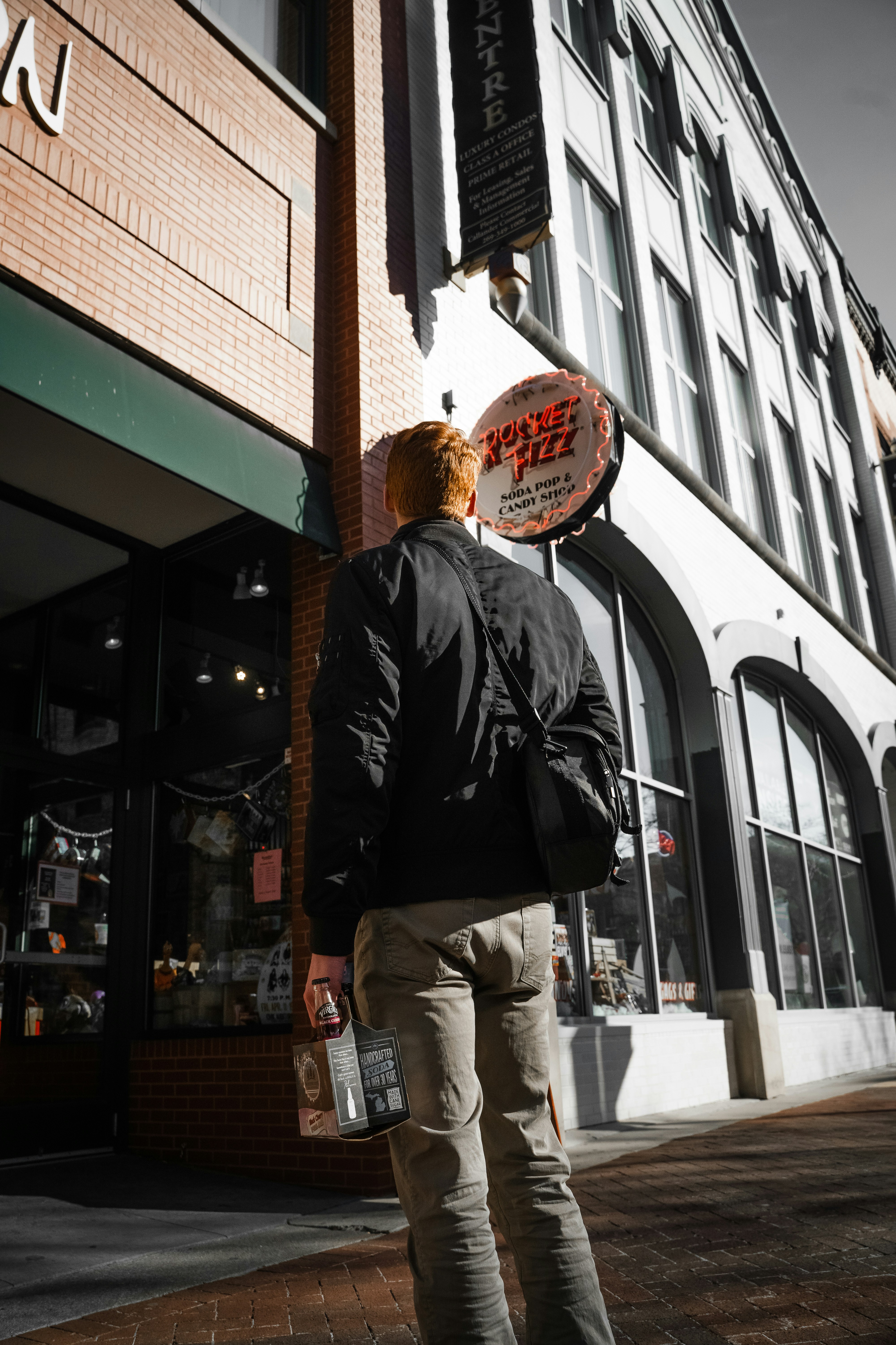Individual standing on a brick sidewalk, gazing up at a vintage candy store sign. The scene captures the essence of urban exploration.