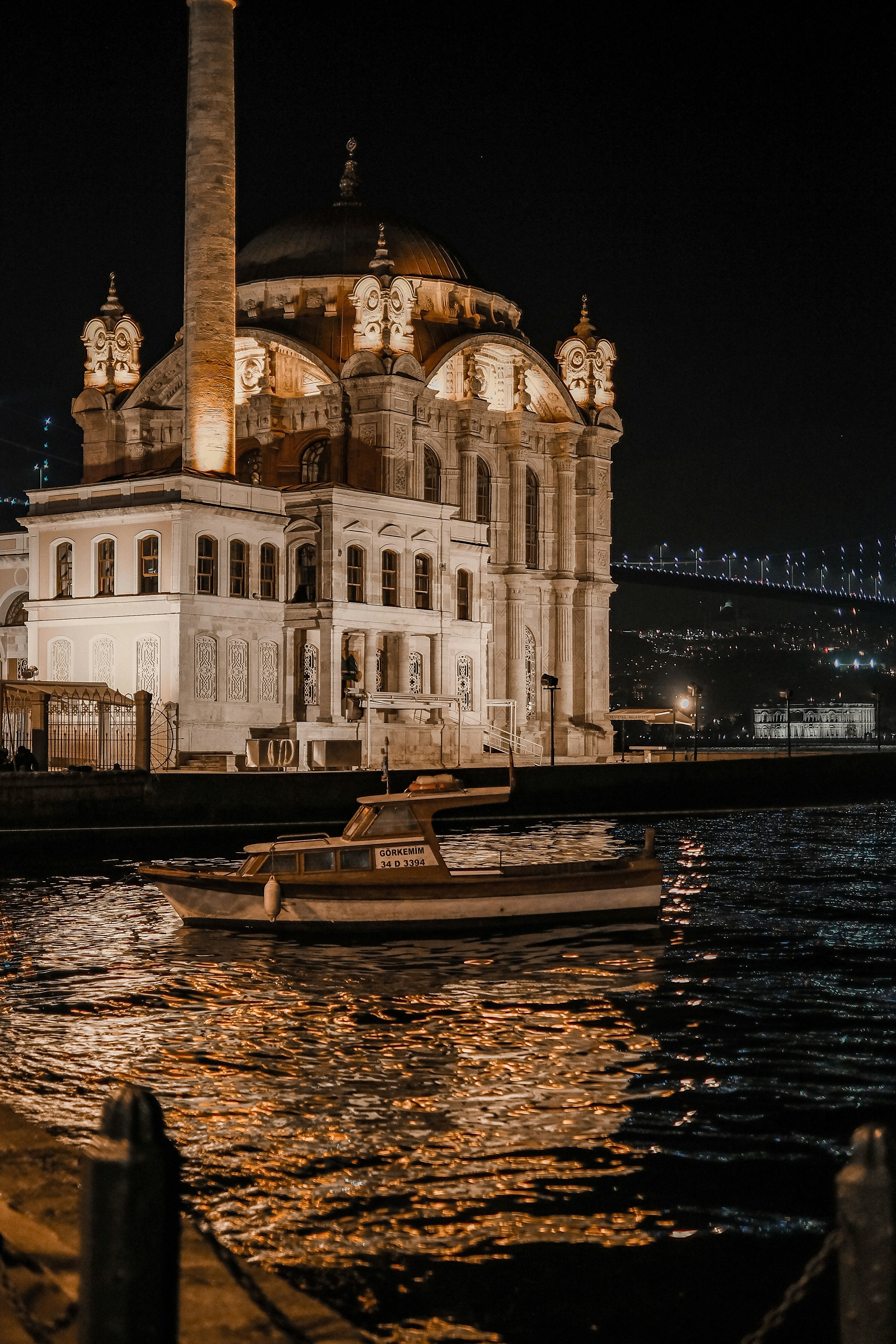 Historic waterfront building illuminated at night, with a boat gently floating in the foreground, reflecting on the water's surface.
