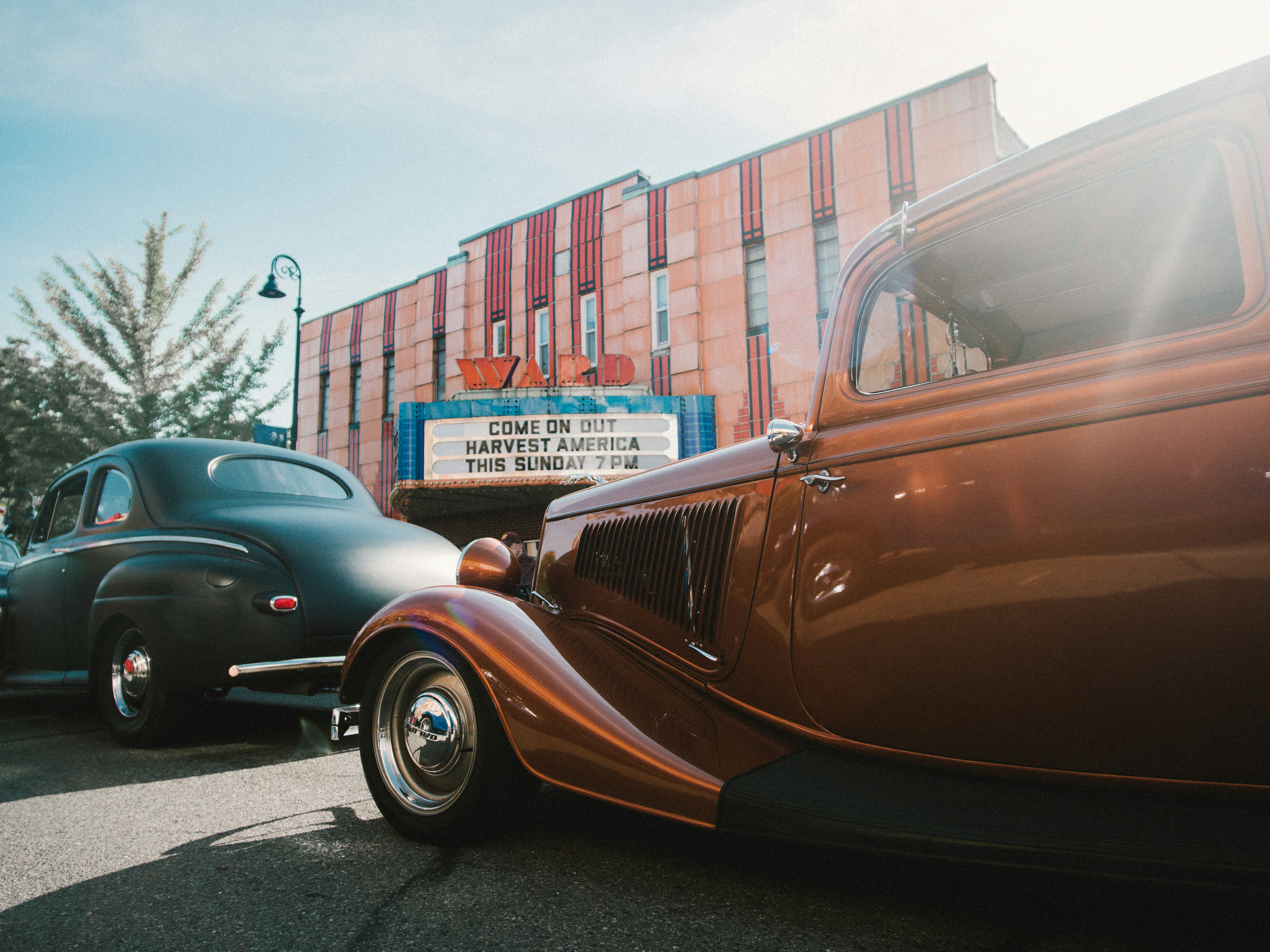 Bronze Curves in the Sun: A Close-Up of a 1930s Coupe Beside a Teal Classic on a City Street
