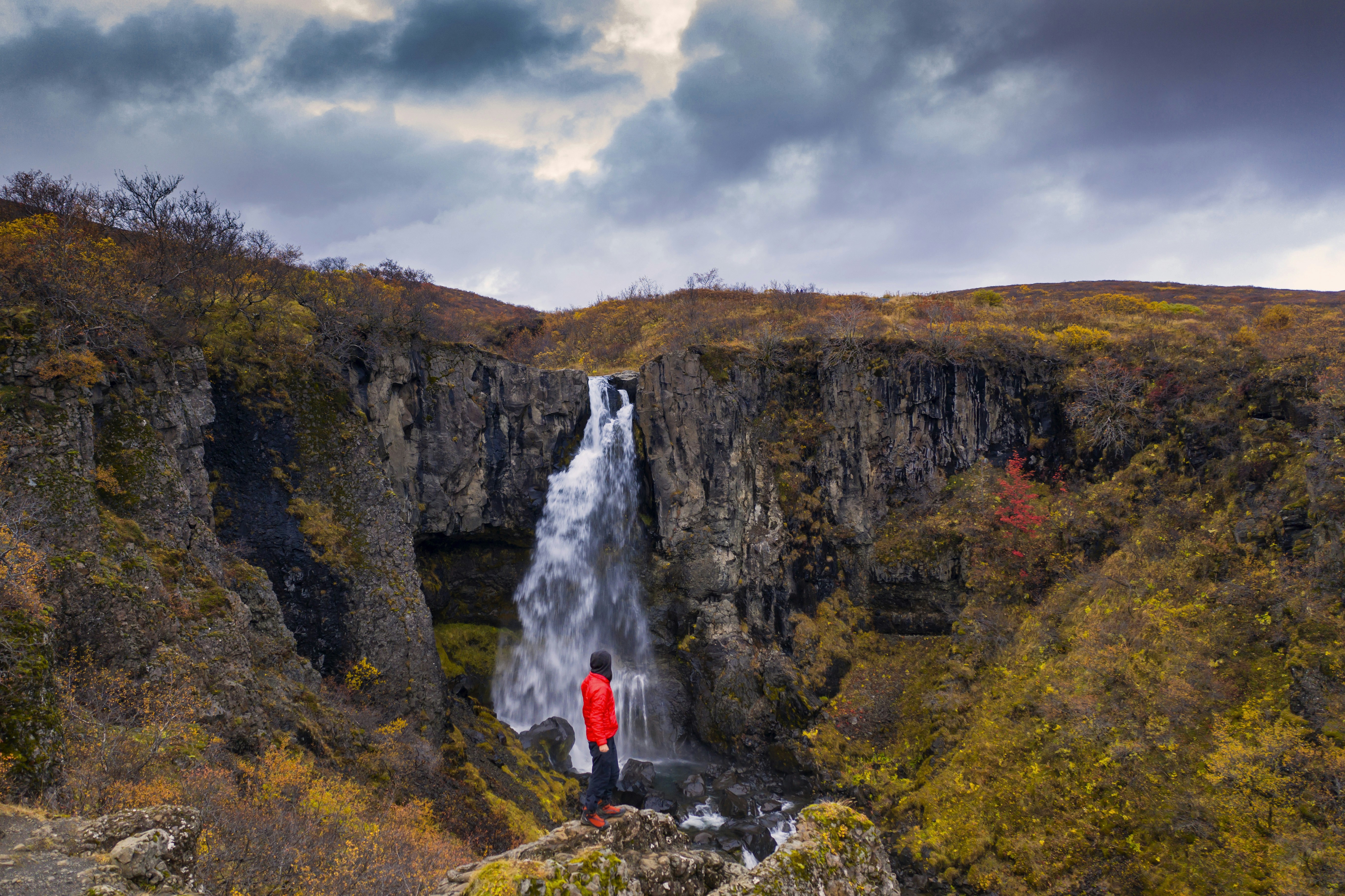 Autumn Cascade: A lone figure at the brink of a rugged waterfall