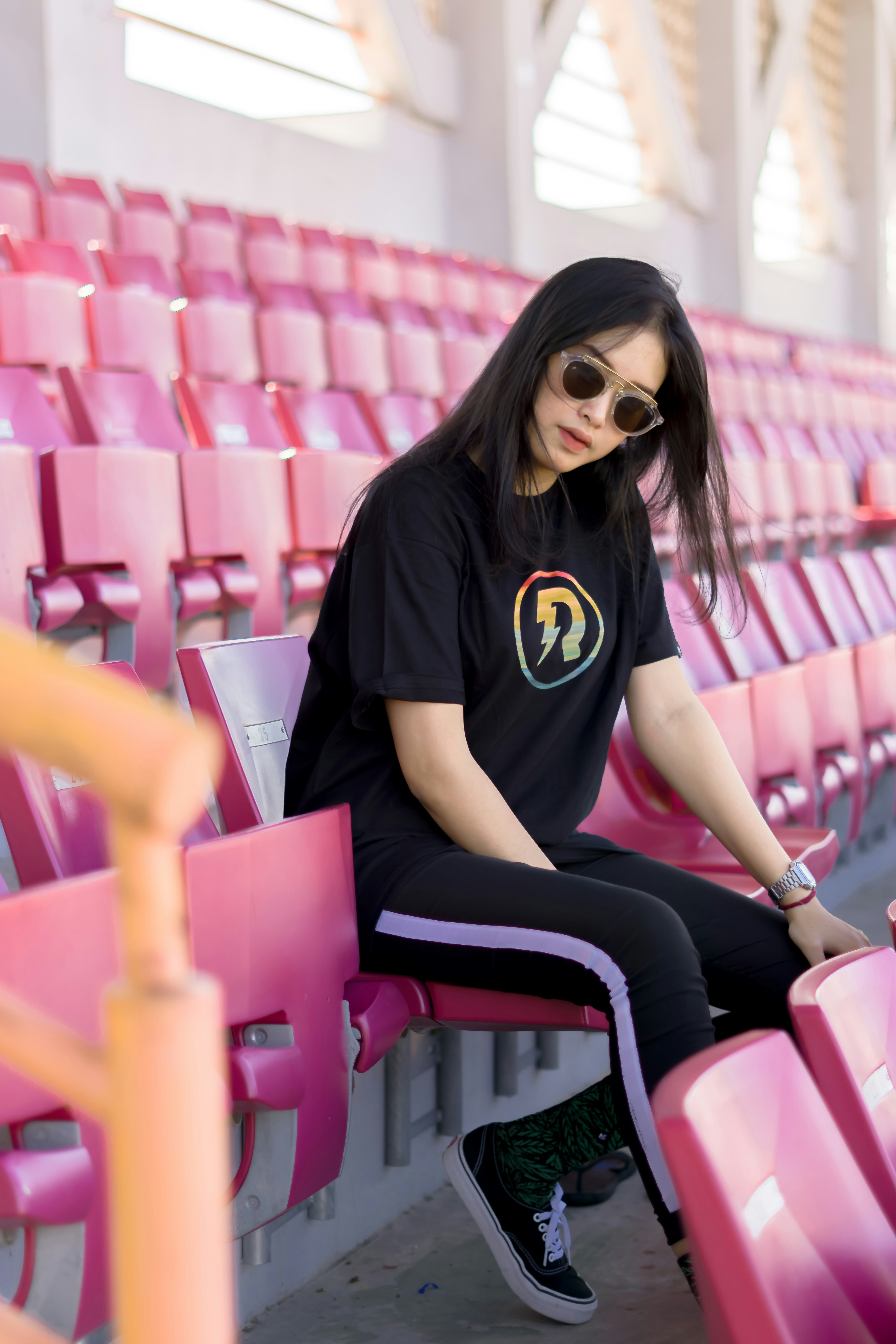 Woman in black tee with sunglasses seated among pink stadium seats