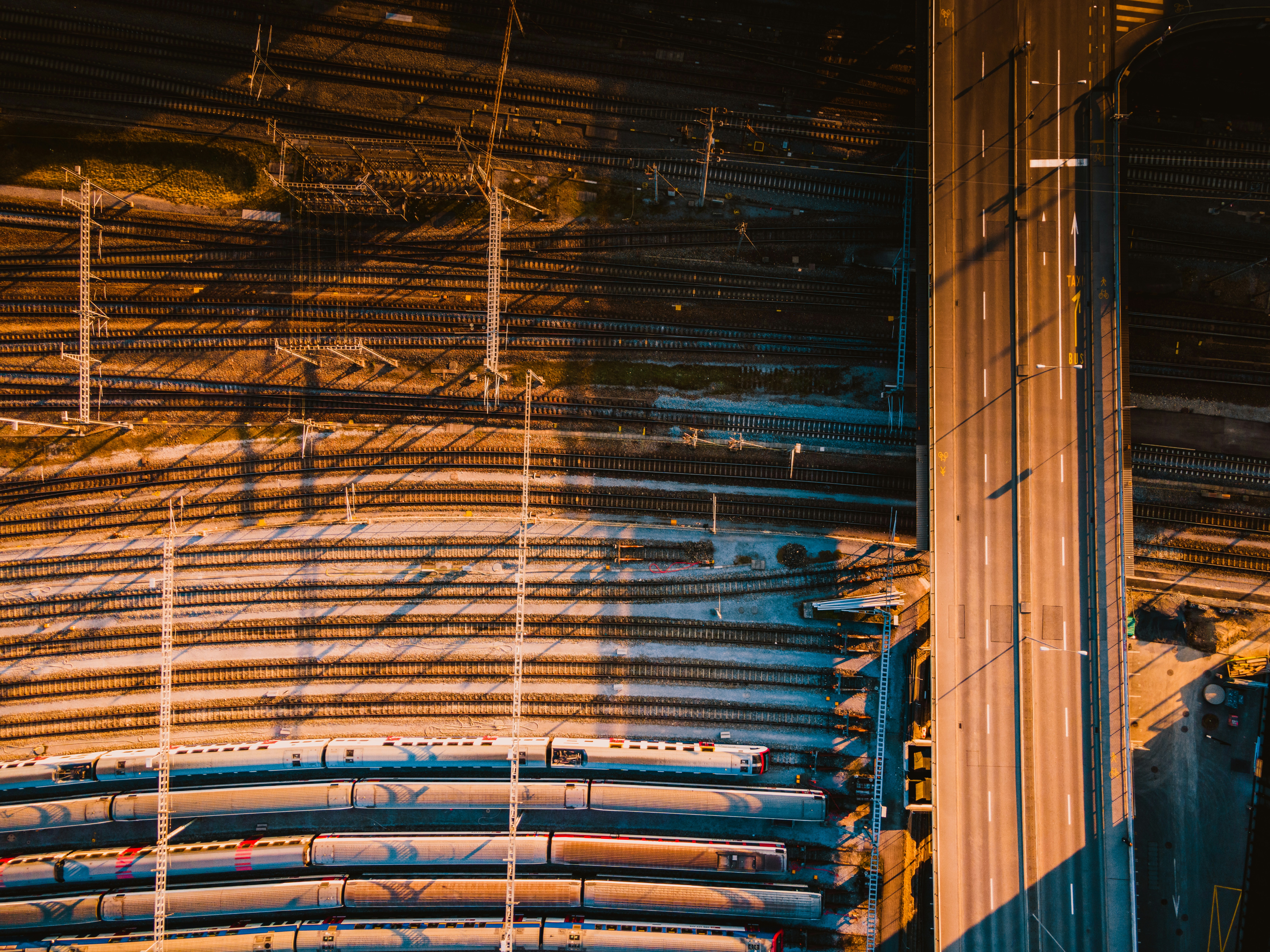 Aerial view of intersecting train tracks and a road bridge, casting long shadows at sunset.