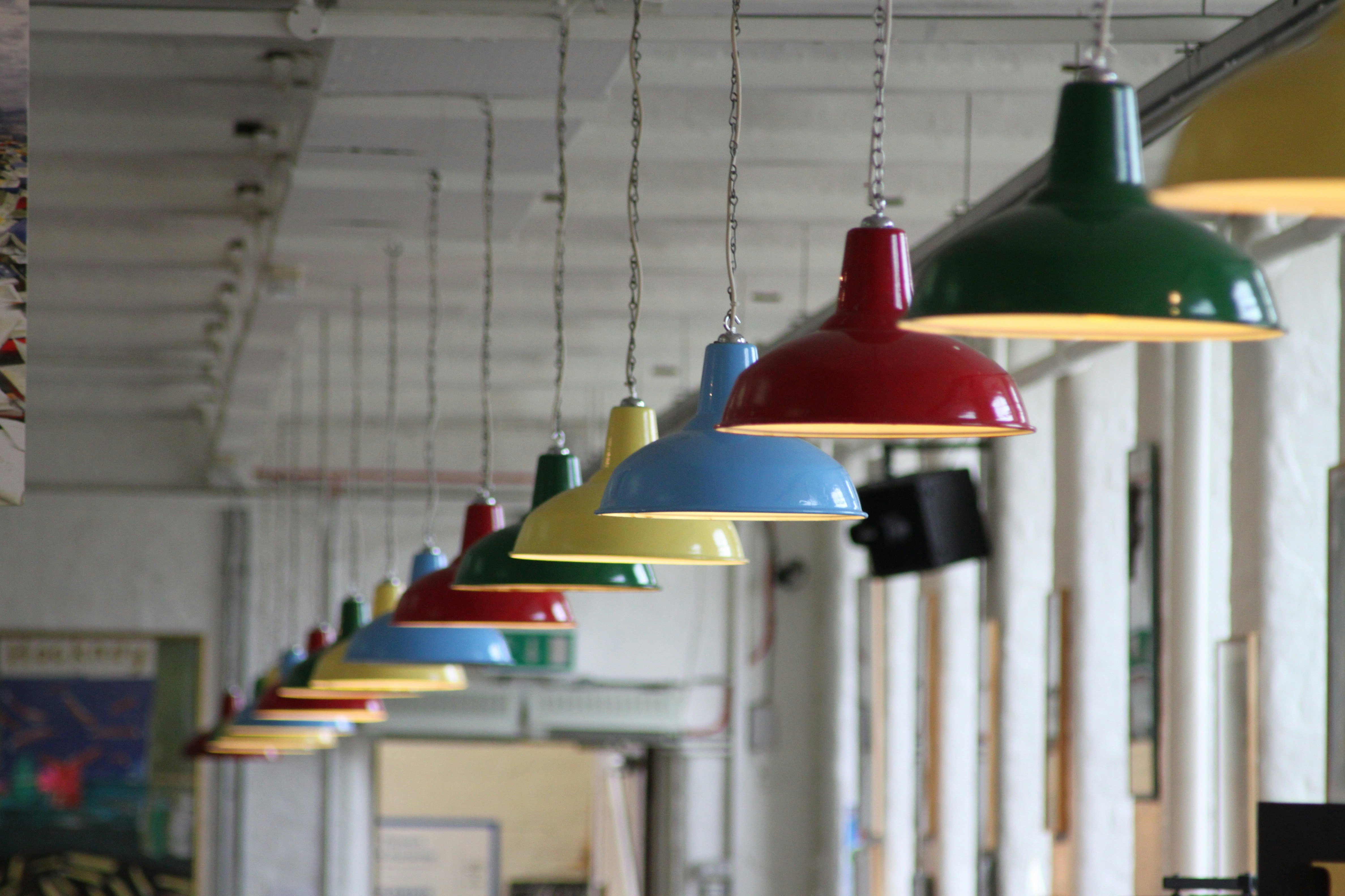 Row of colorful industrial pendant lights hanging from a ceiling in a spacious interior.