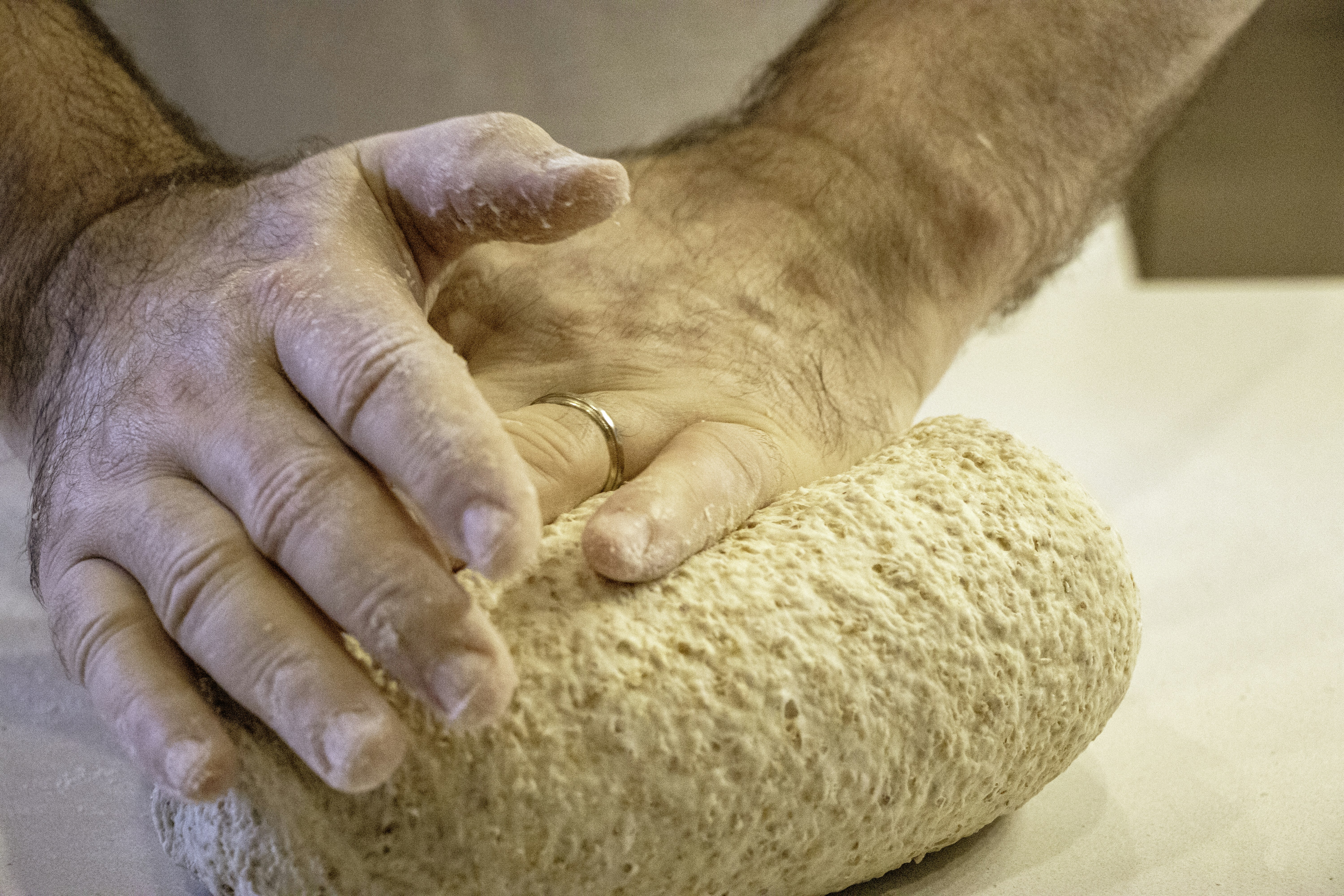 Hands skillfully kneading a loaf of whole grain dough, showcasing the tactile process of bread-making.