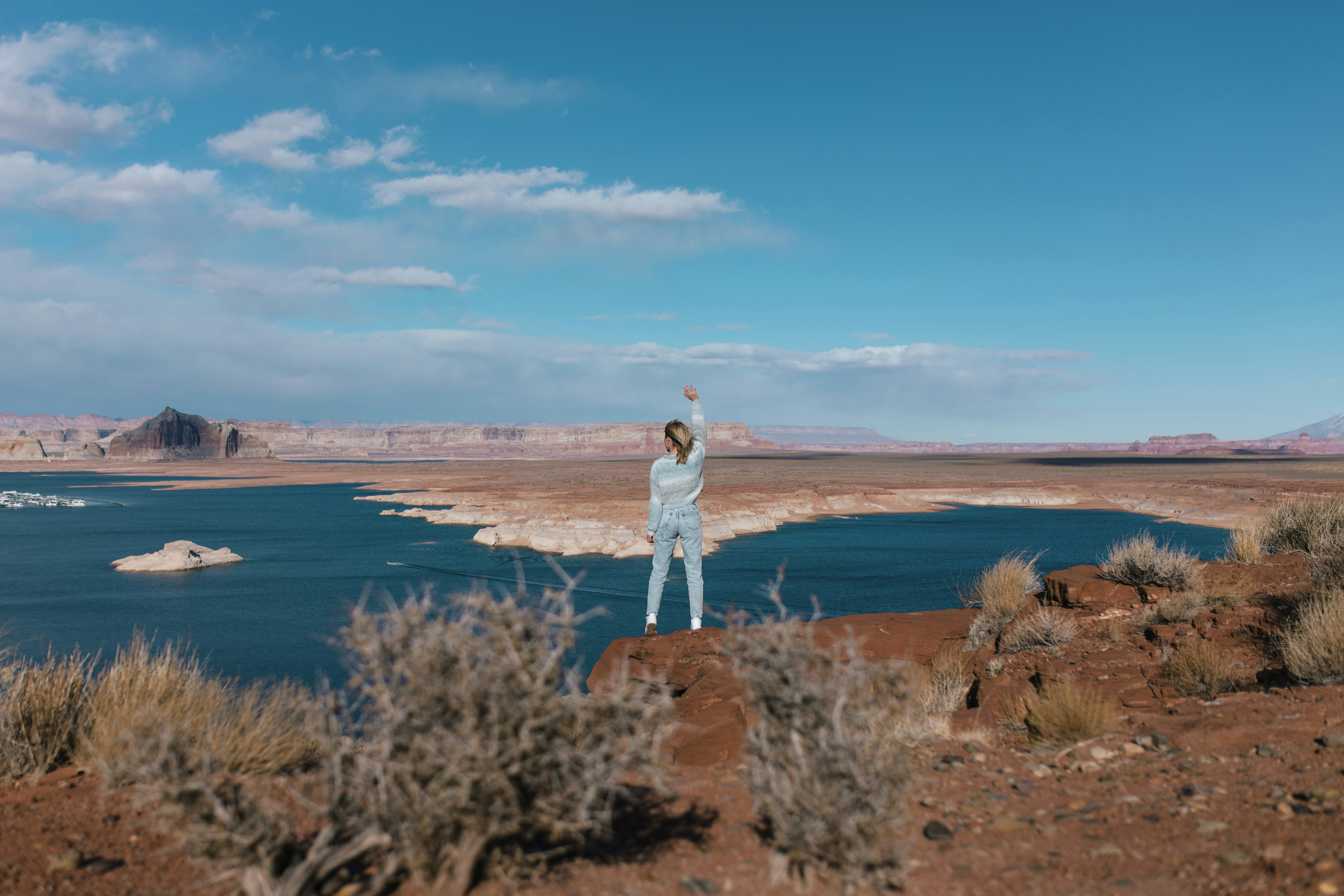 Person standing on a rocky overlook, gazing at a vast desert lake under a vibrant blue sky.