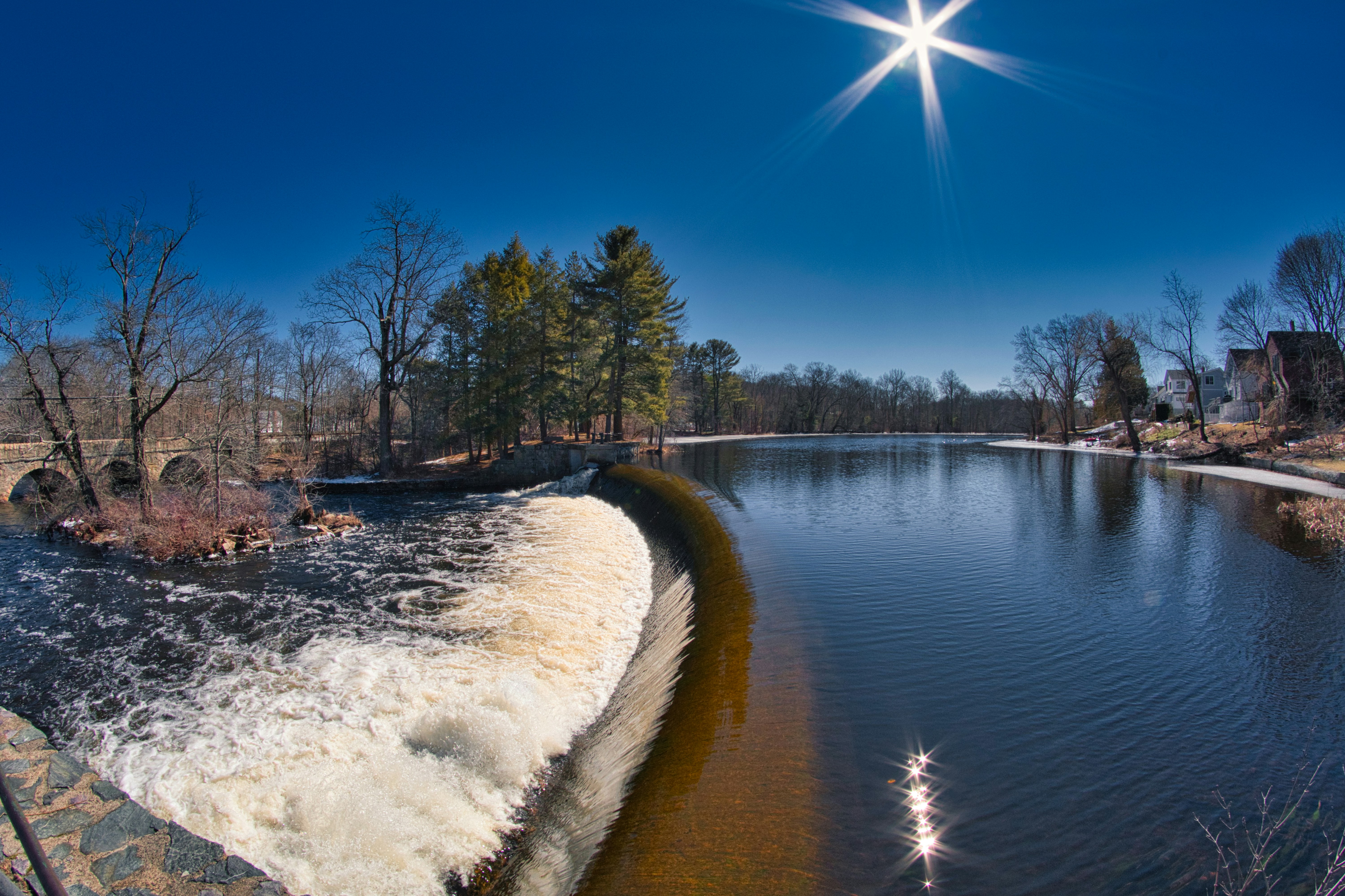 Curved river with flowing water bordered by trees under a bright sun.