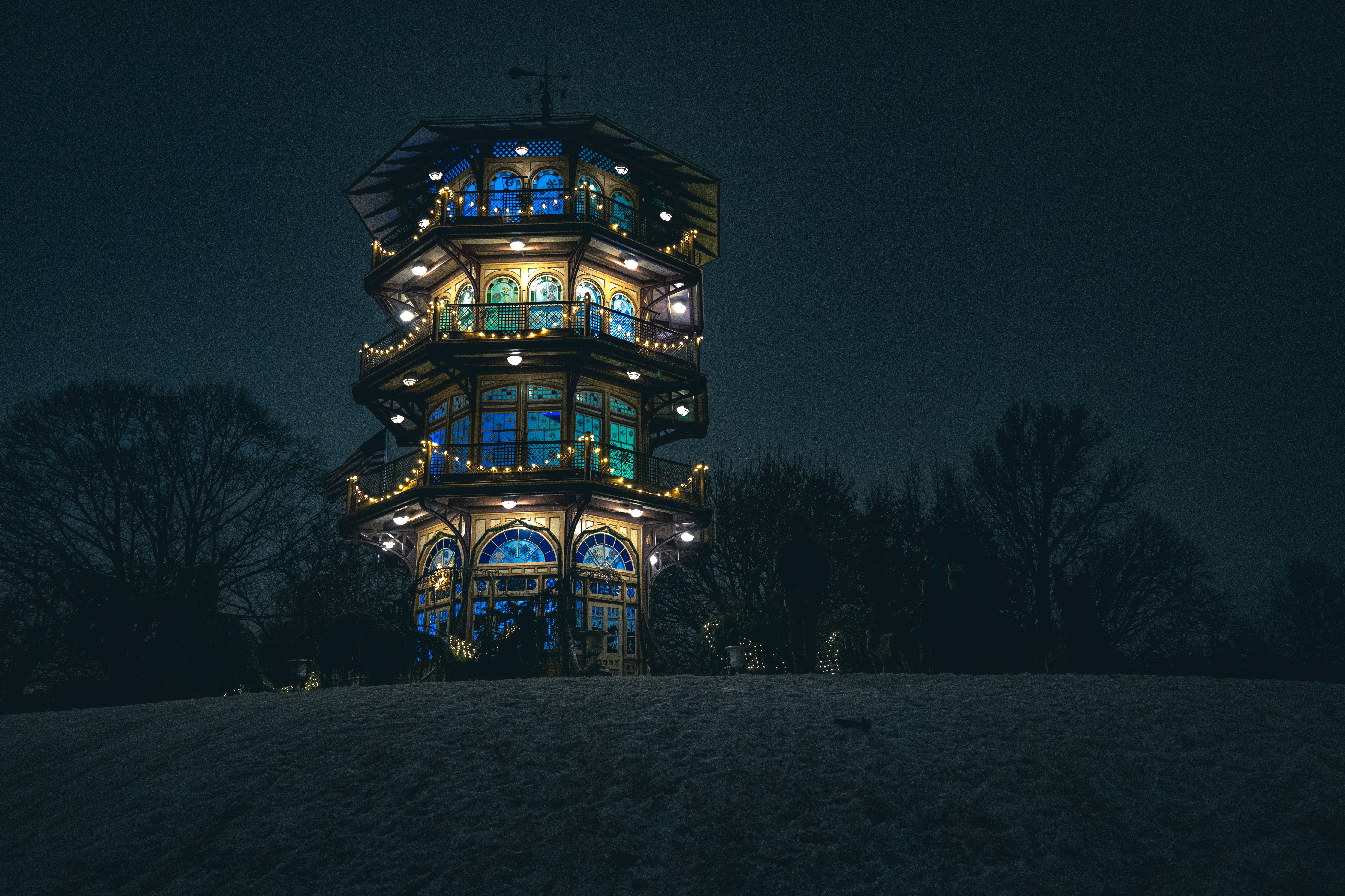 Multi-tiered pagoda with blue lighting standing against a dark, tree-lined backdrop at night.