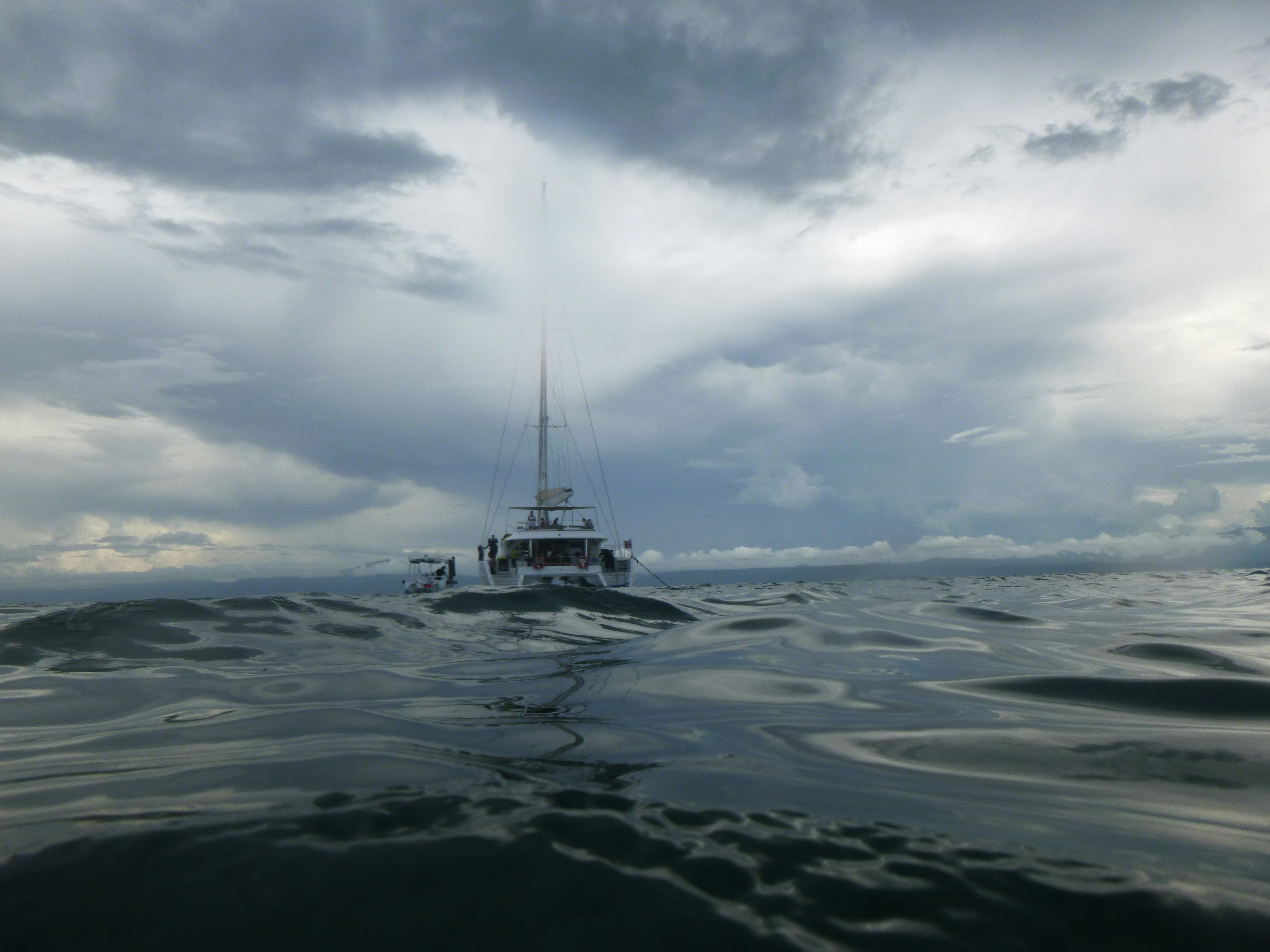 Sailboat navigating through gently rippling waters under a dramatic sky filled with clouds.