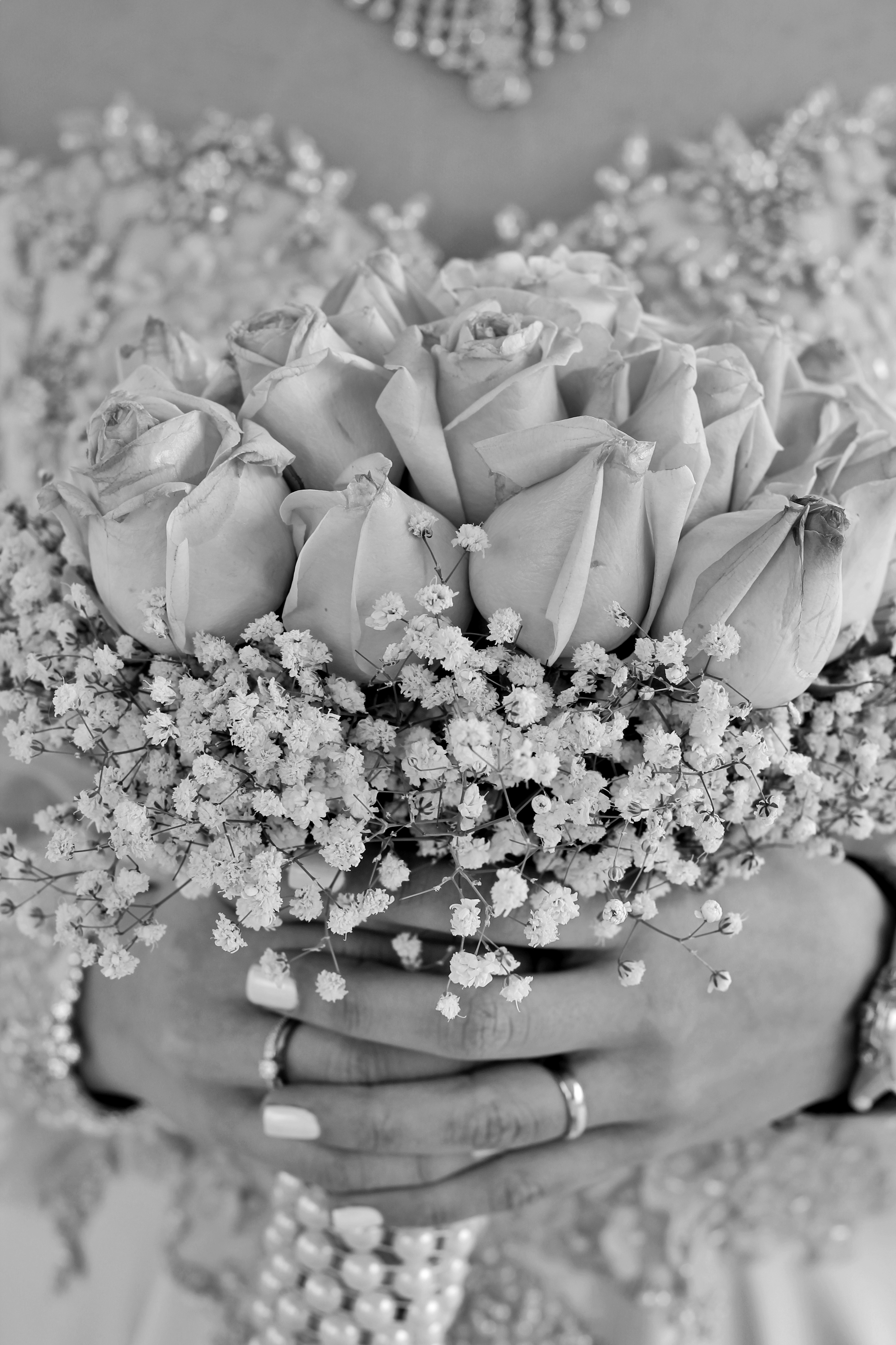 Bouquet of pale roses adorned with delicate gypsophila, held gracefully by a hand decorated with rings and pearls.