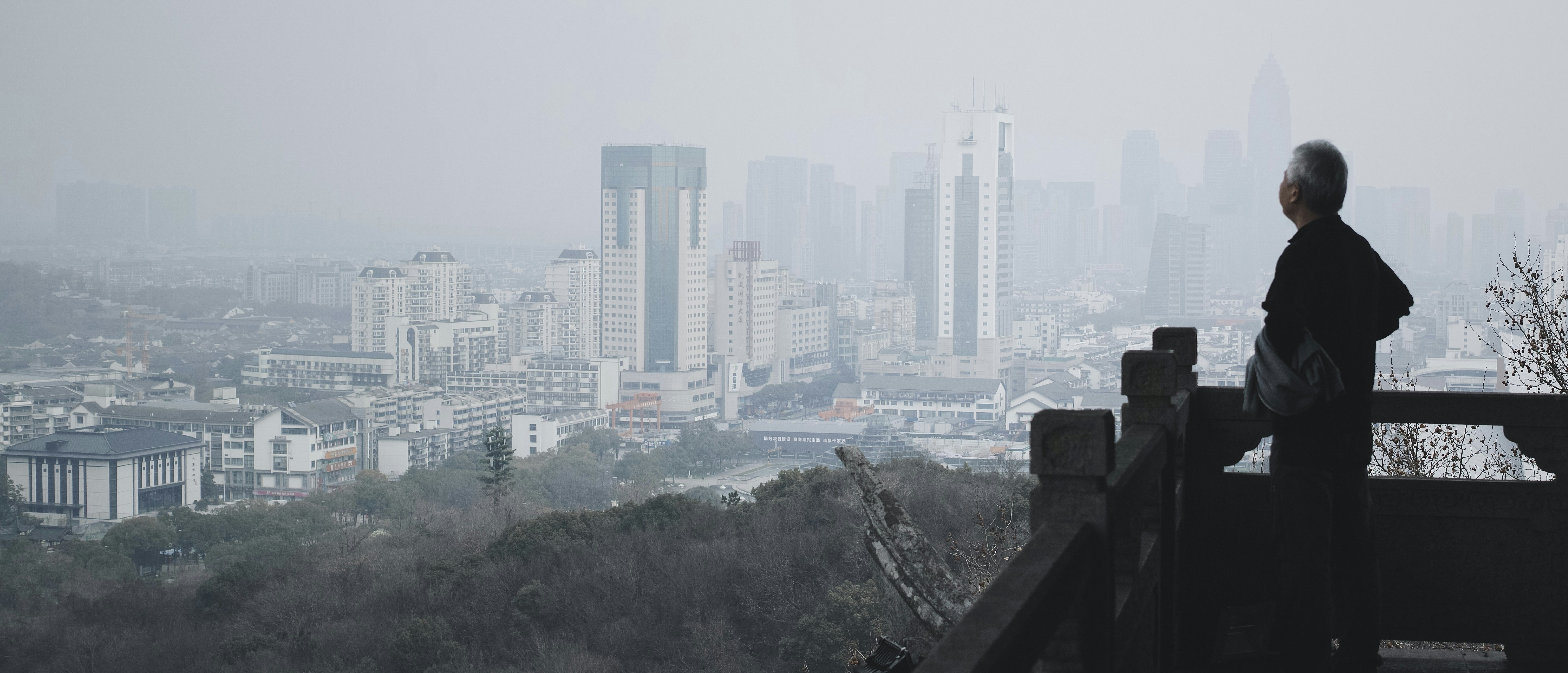 Silhouette of a person on a balcony overlooking a foggy cityscape.