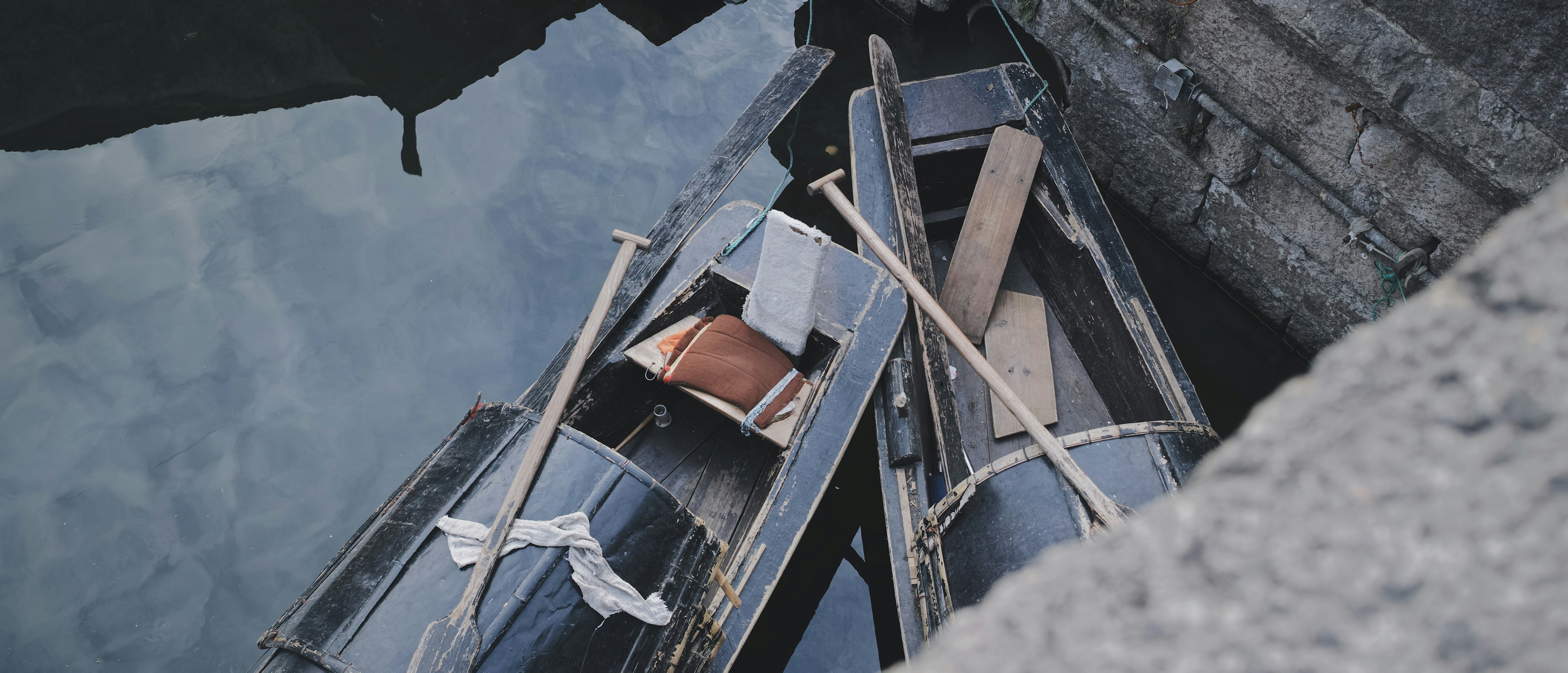 Two weathered boats resting side by side against a stone wall, reflecting the calm water's surface.