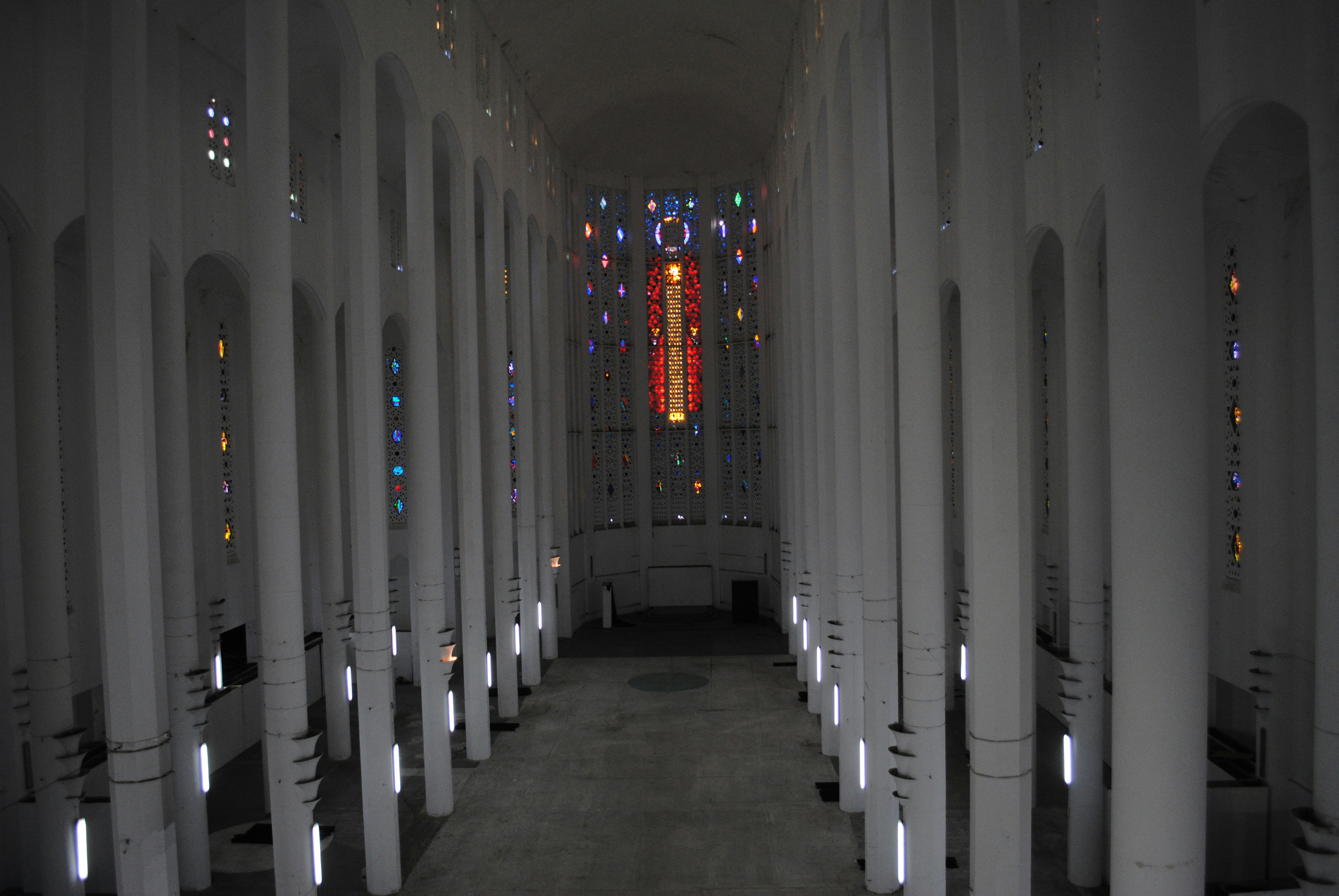 White concrete hallway with vibrant red stained glass centerpiece and ambient lighting.