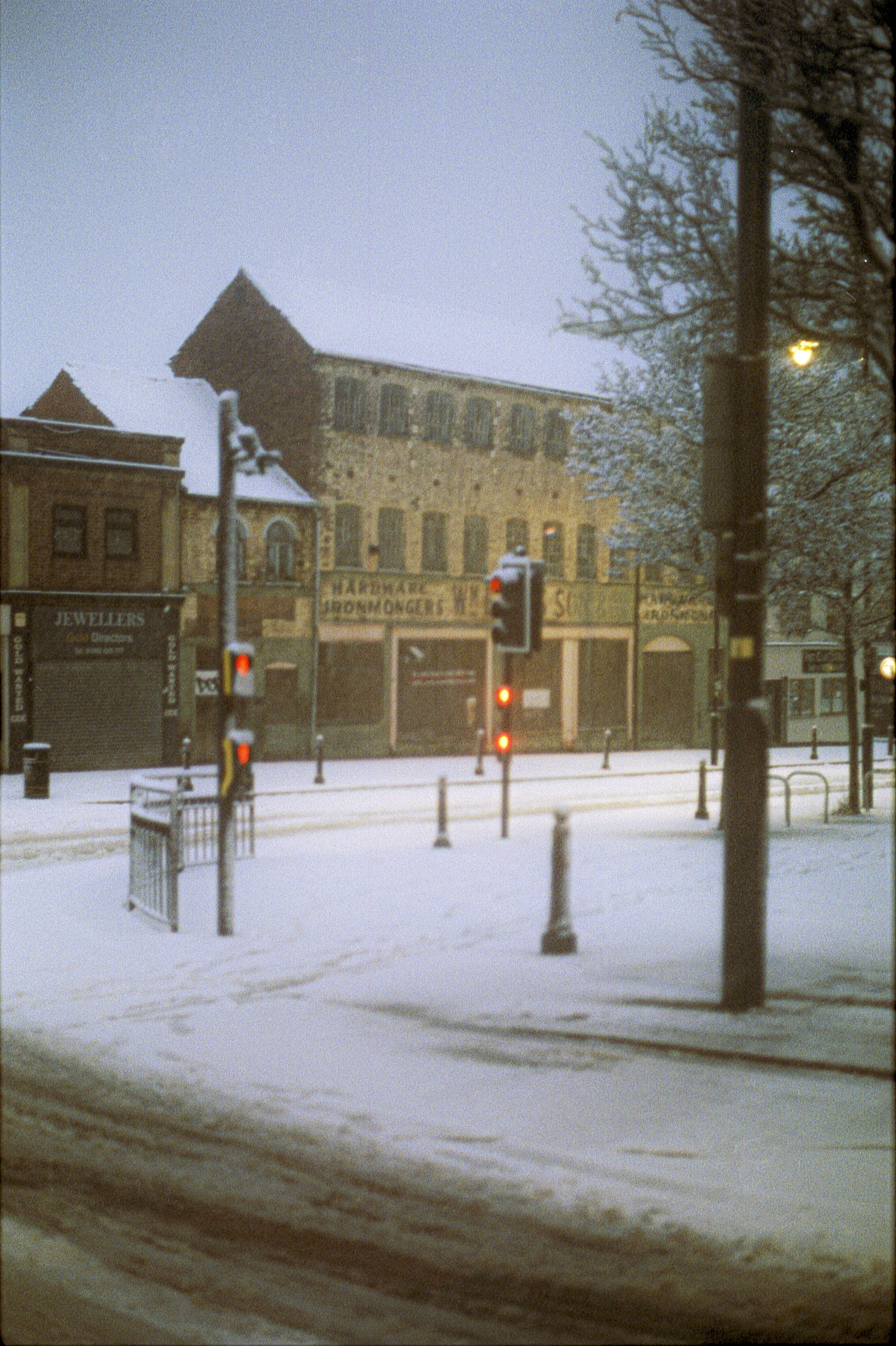 Snow-covered urban street scene featuring historical buildings and traffic signals during twilight.
