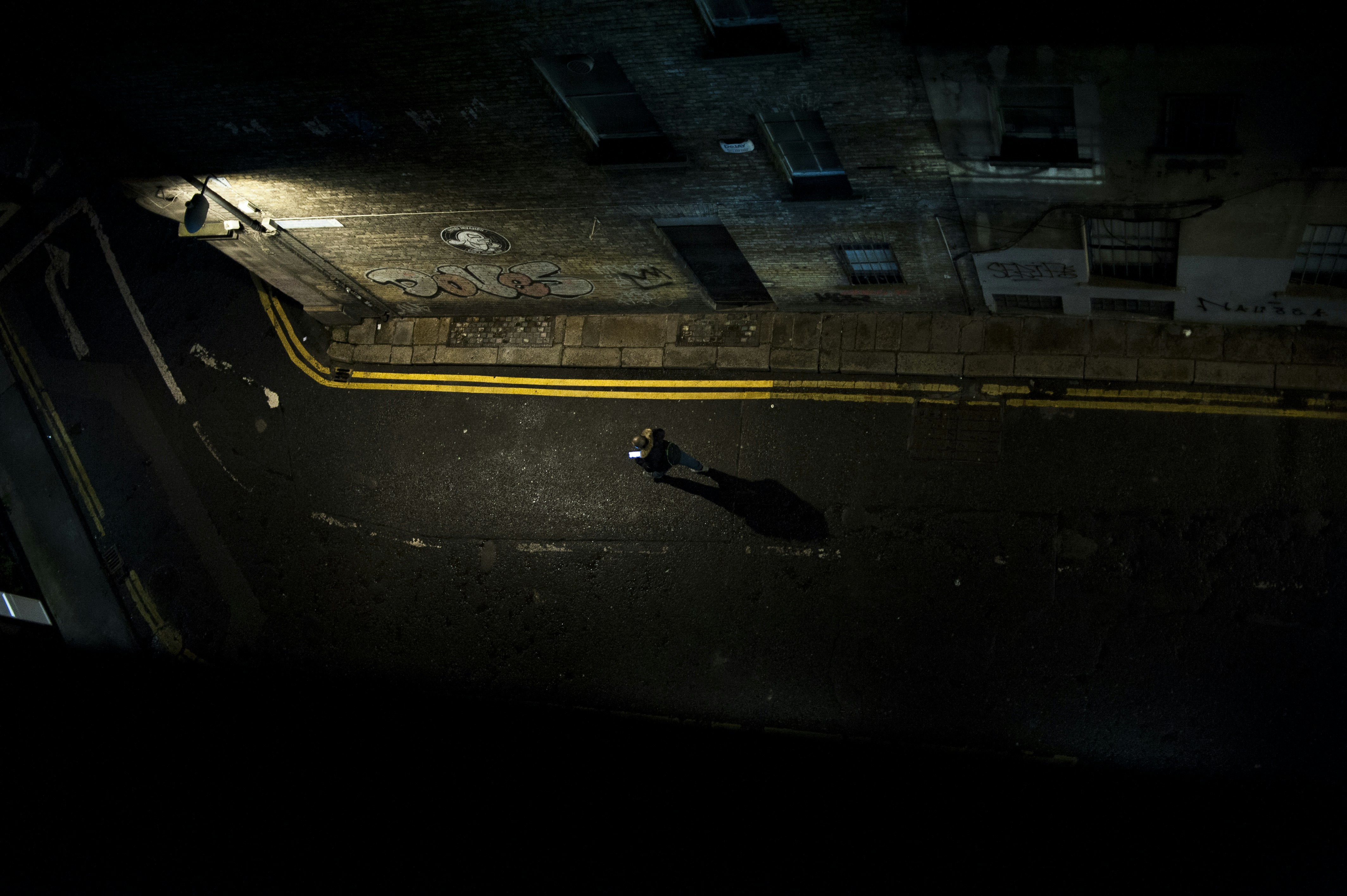 Person walking alone on a dimly lit street at night, casting a long shadow.