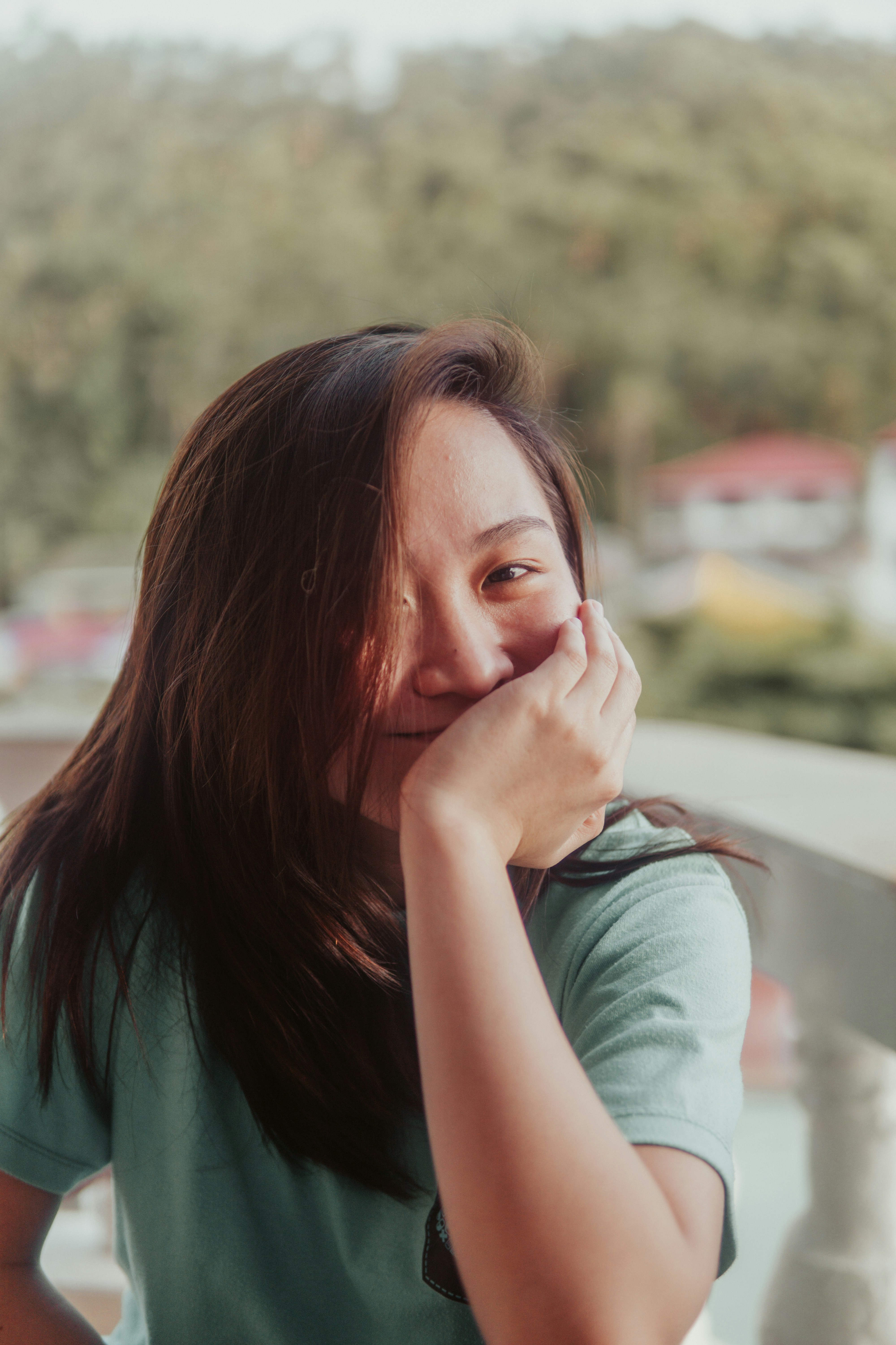 A young woman playfully resting her chin on her hand, exuding warmth and happiness against a blurred natural backdrop.