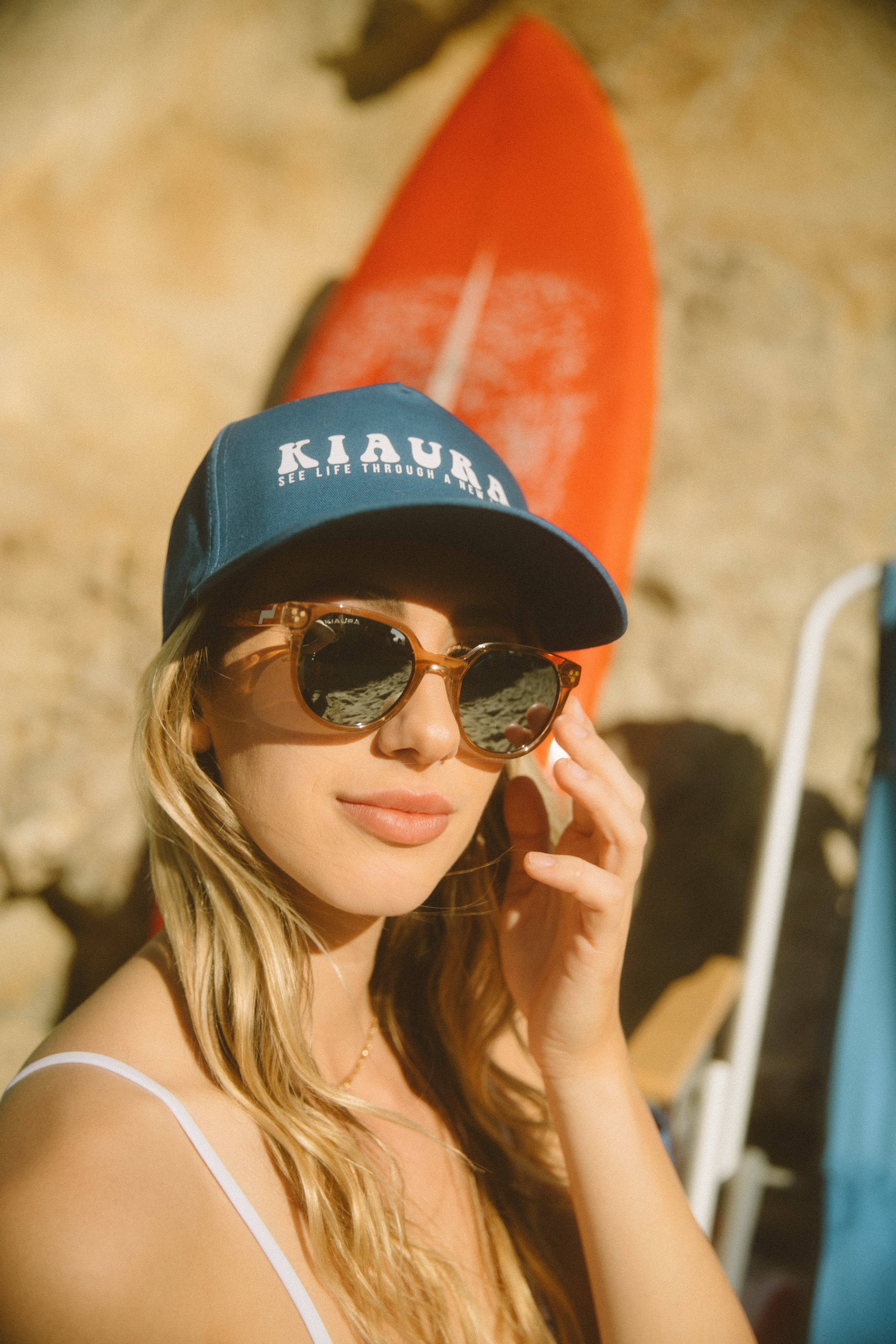 Sunlit Shore Portrait: Blue Cap, Sunglasses, and a Crimson Surfboard Backdrop