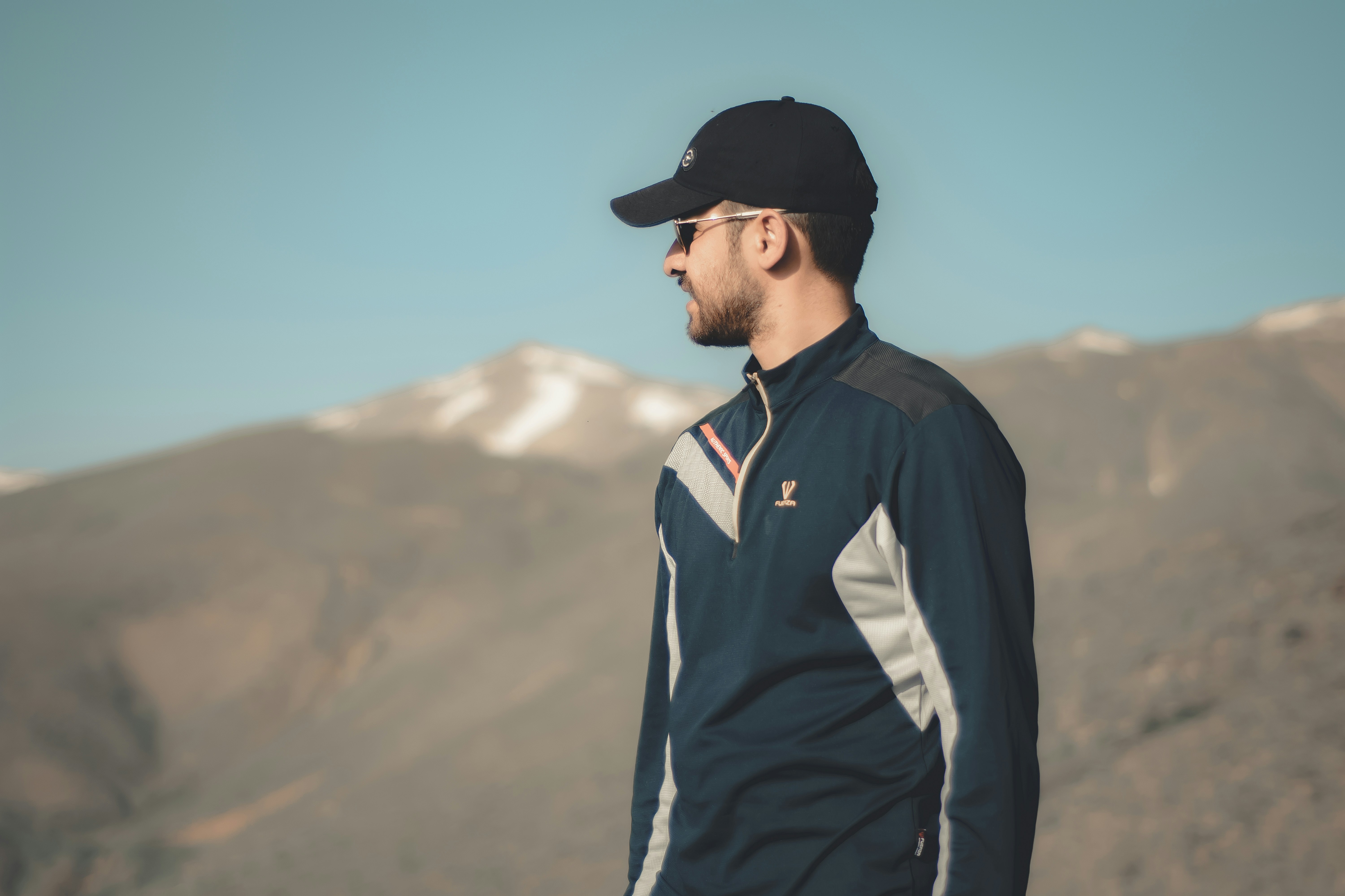 Man gazing thoughtfully at the distant mountain landscape, dressed in outdoor gear. The scene captures a serene connection with nature.
