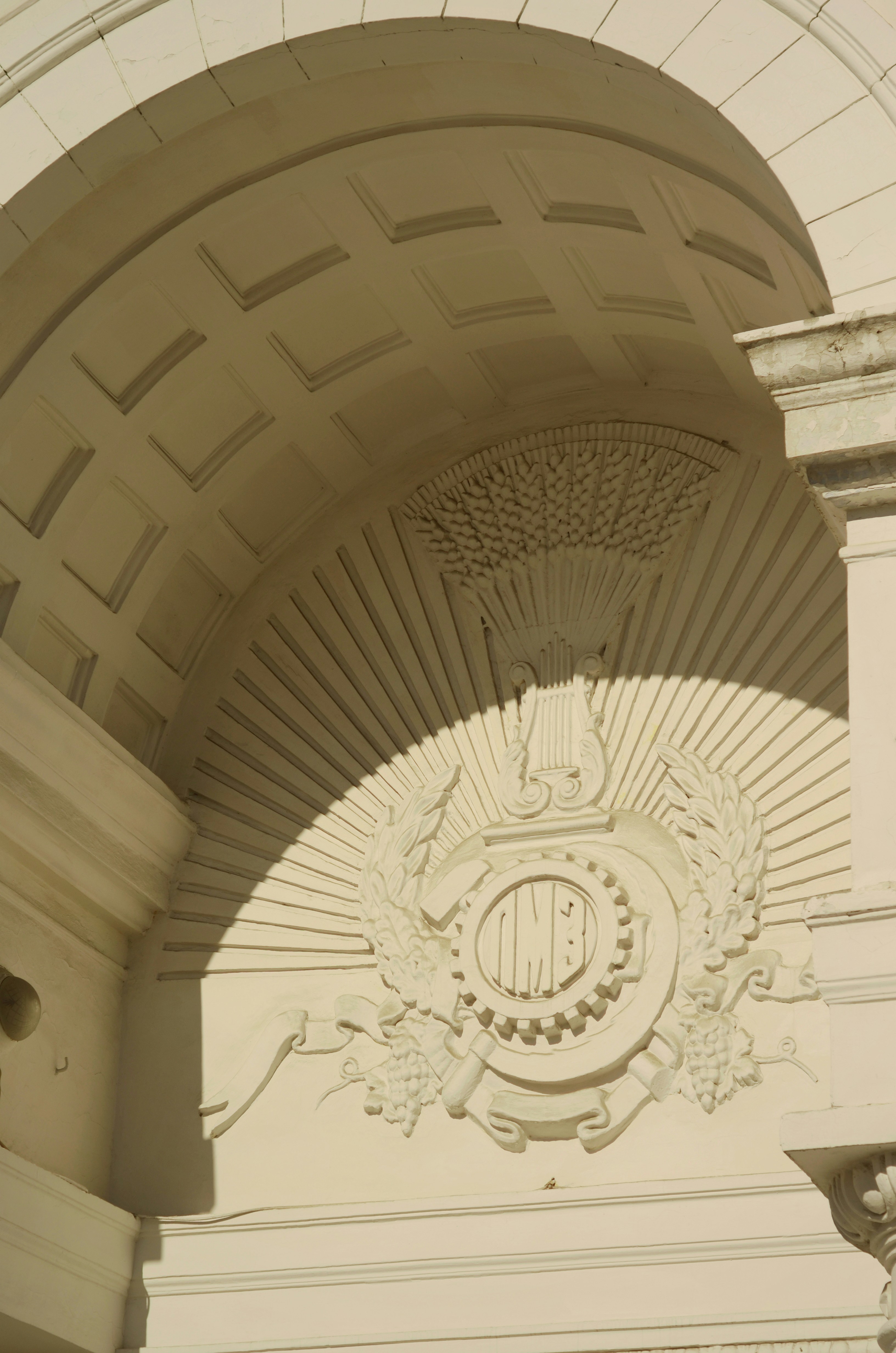 Intricate relief sculpture featuring an emblem with rays and decorative elements, set against a textured archway.