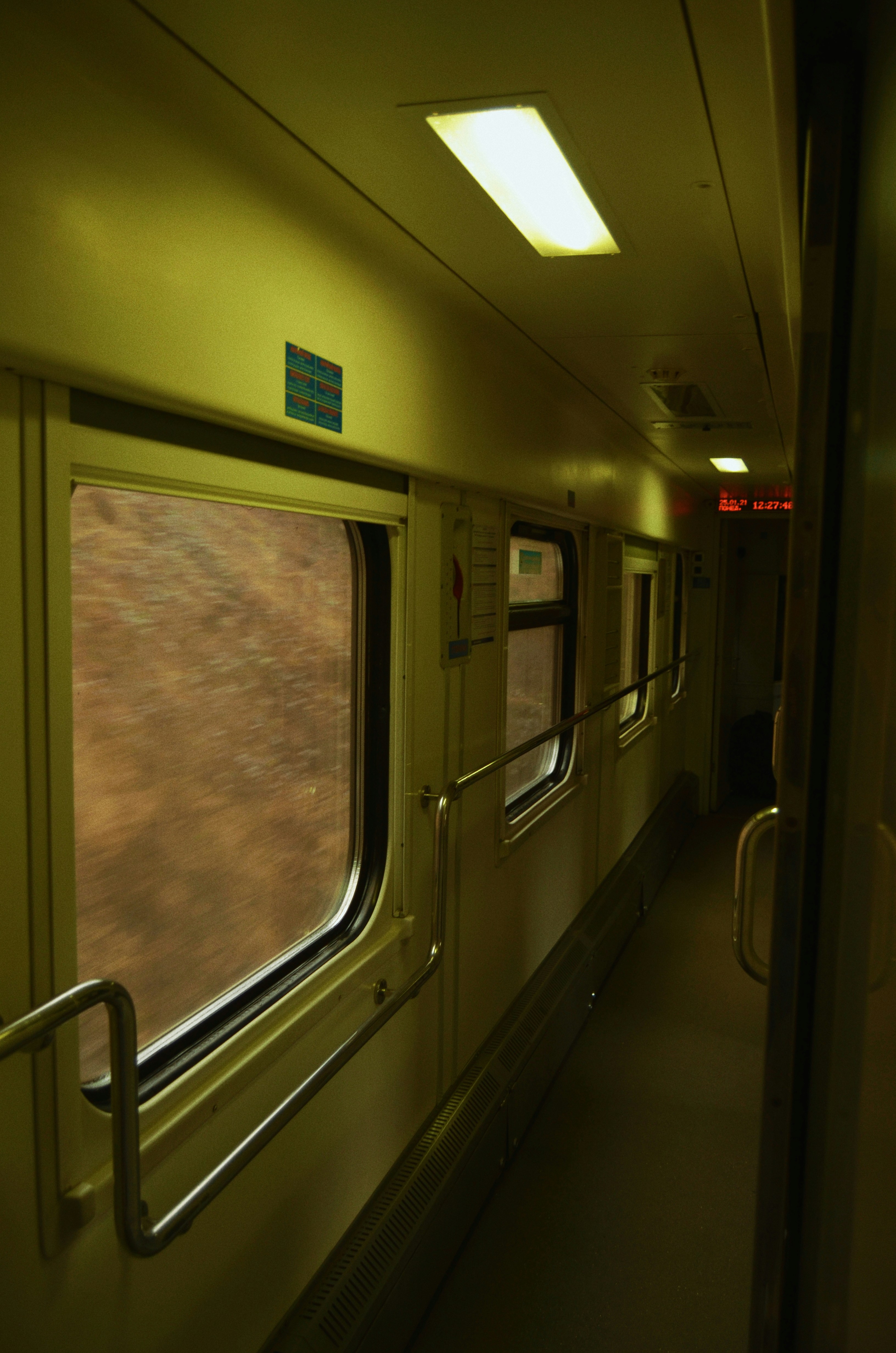 Interior view of a train corridor with windows showcasing the passing landscape, illuminated by overhead lights.