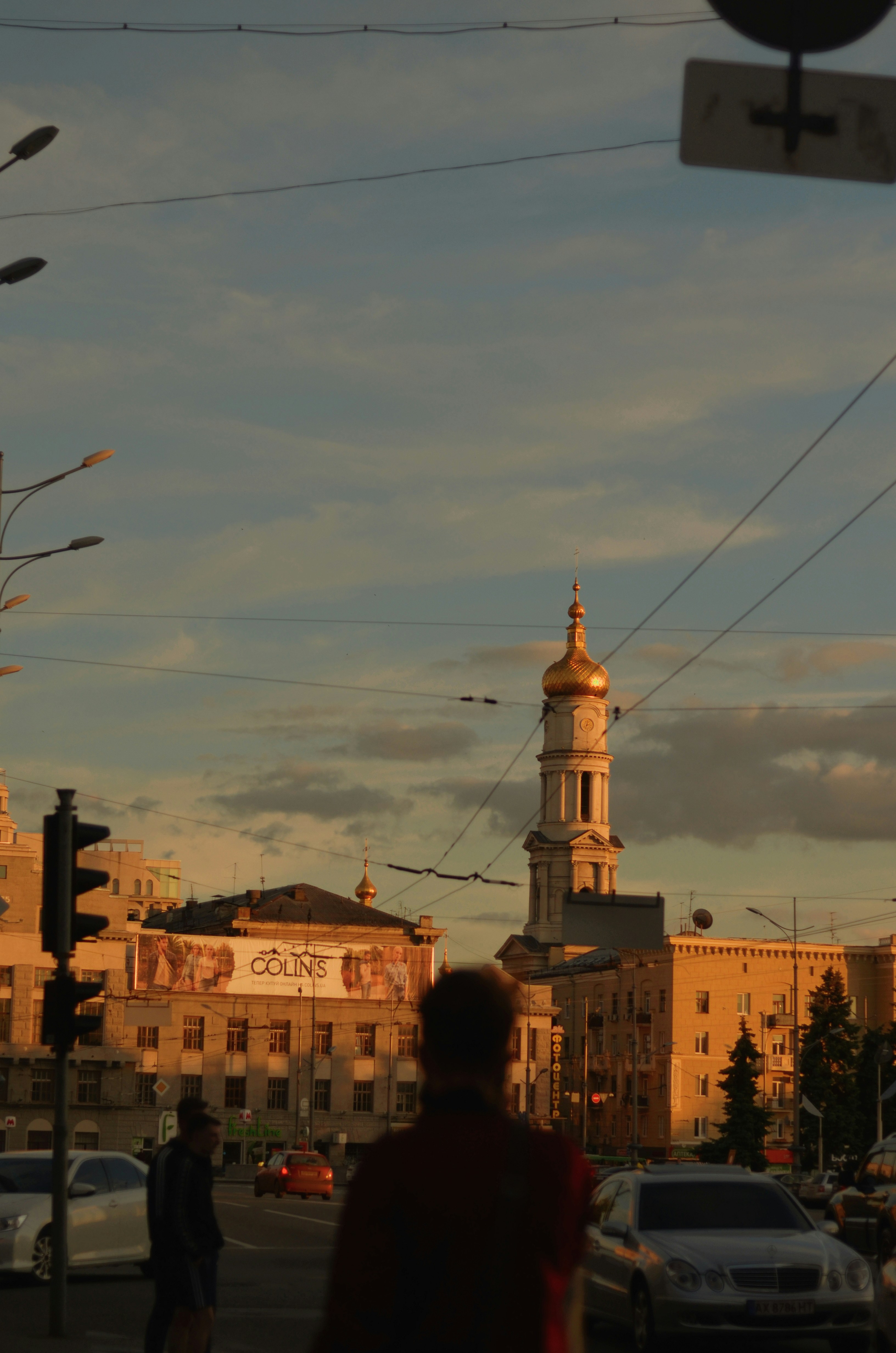 A historic building with a golden dome stands prominently against a dusky sky, while pedestrians traverse the bustling street below.