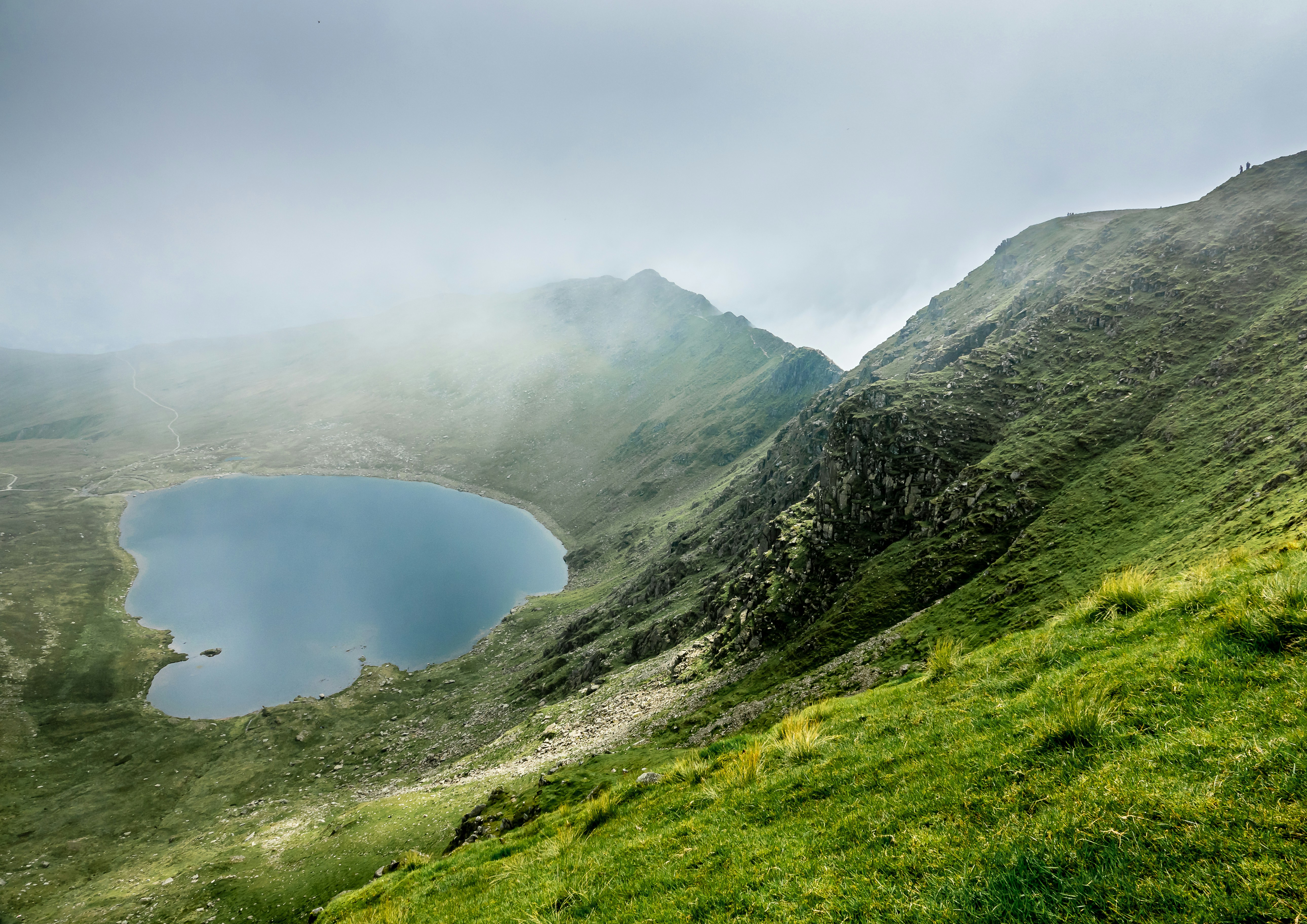 Serene mountain landscape featuring a tranquil lake surrounded by lush greenery and misty hills. The atmosphere conveys a sense of calm and isolation.