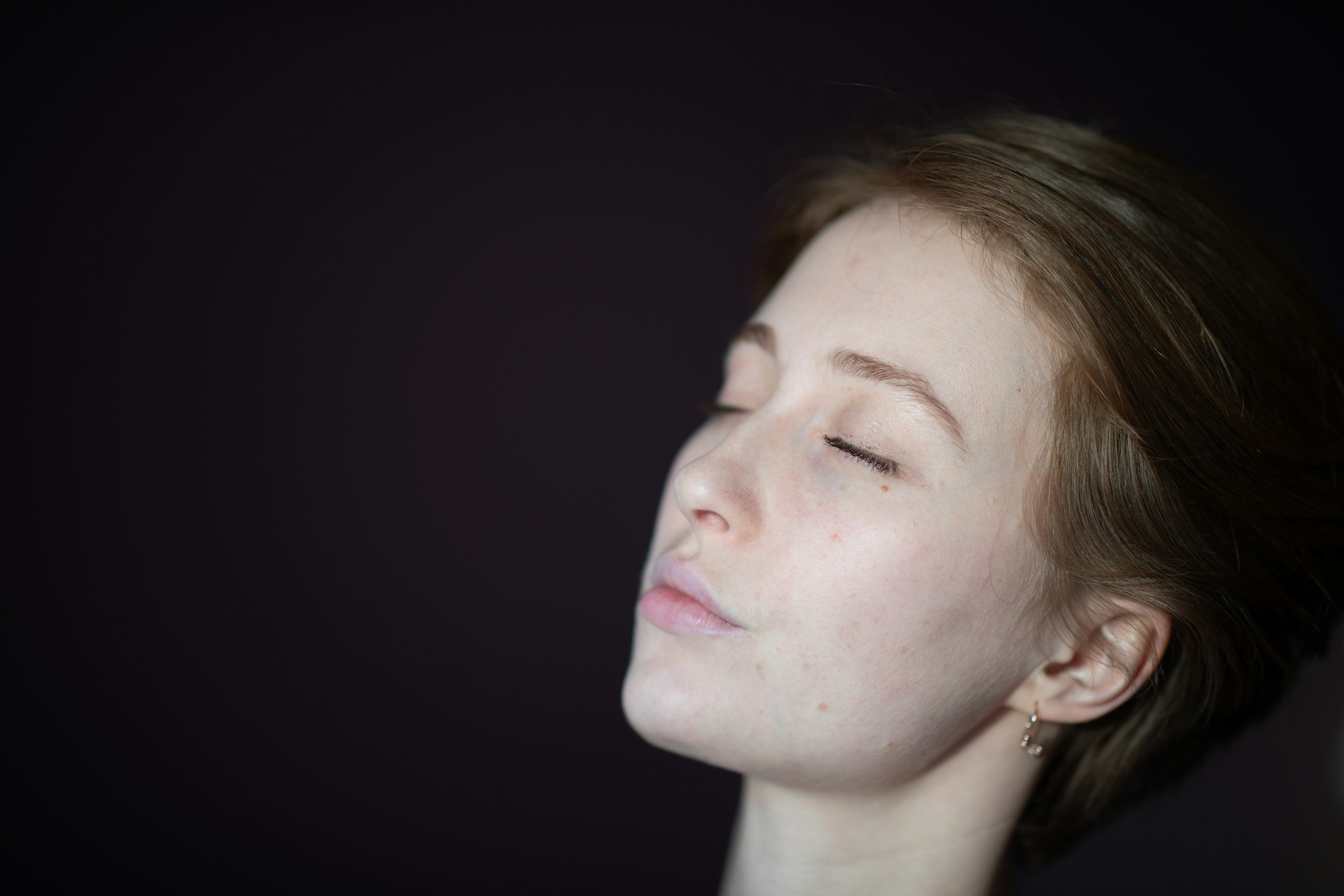 A serene portrait of a woman with closed eyes, exuding calmness against a soft, dark background.