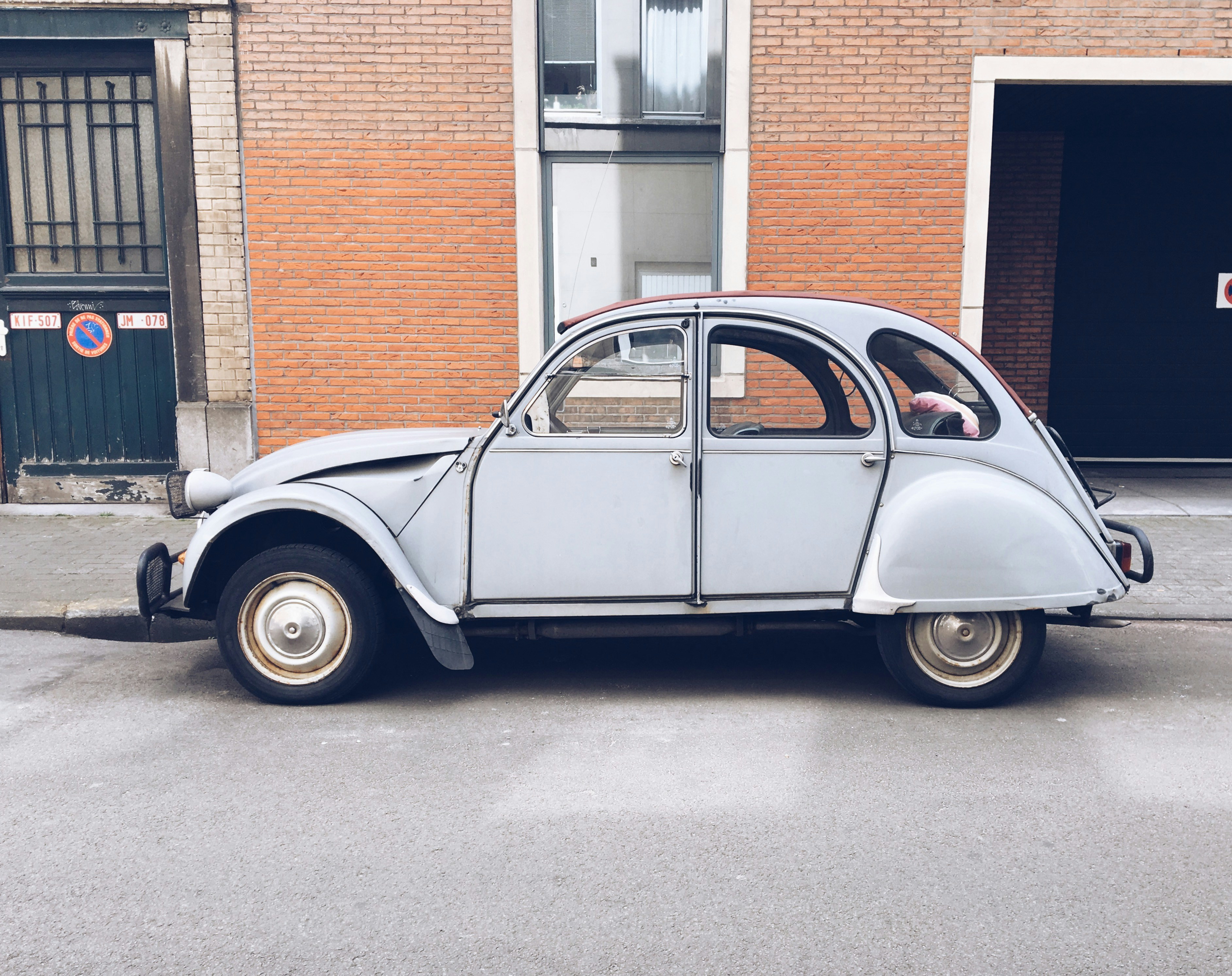 A vintage retro grey car parked outside in the city centre of Brussels, Belgium in front of an orange brick wall. Oldtimer Citroen 2cv6.