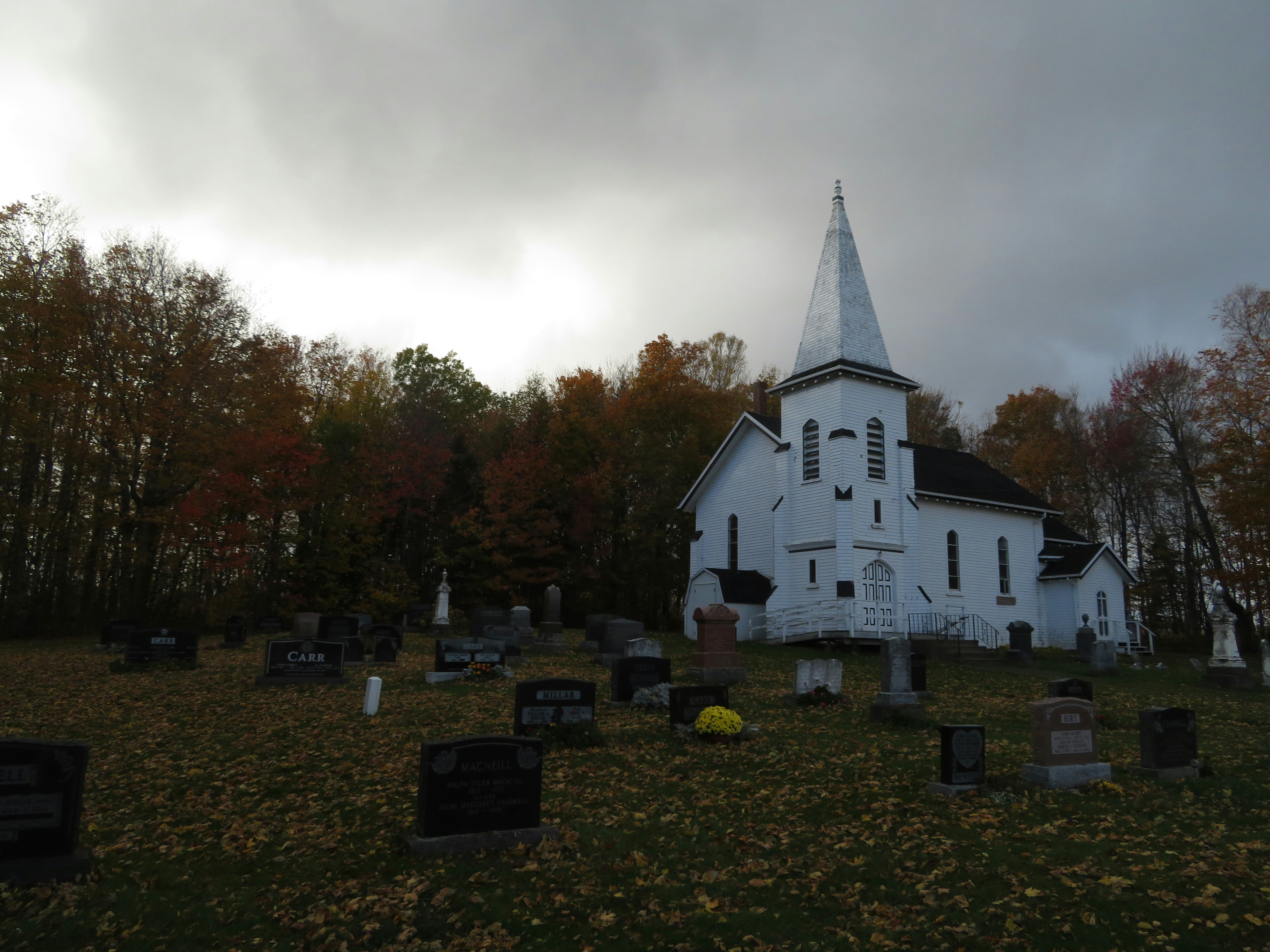 Historic church surrounded by gravestones and vibrant autumn foliage under a cloudy sky.