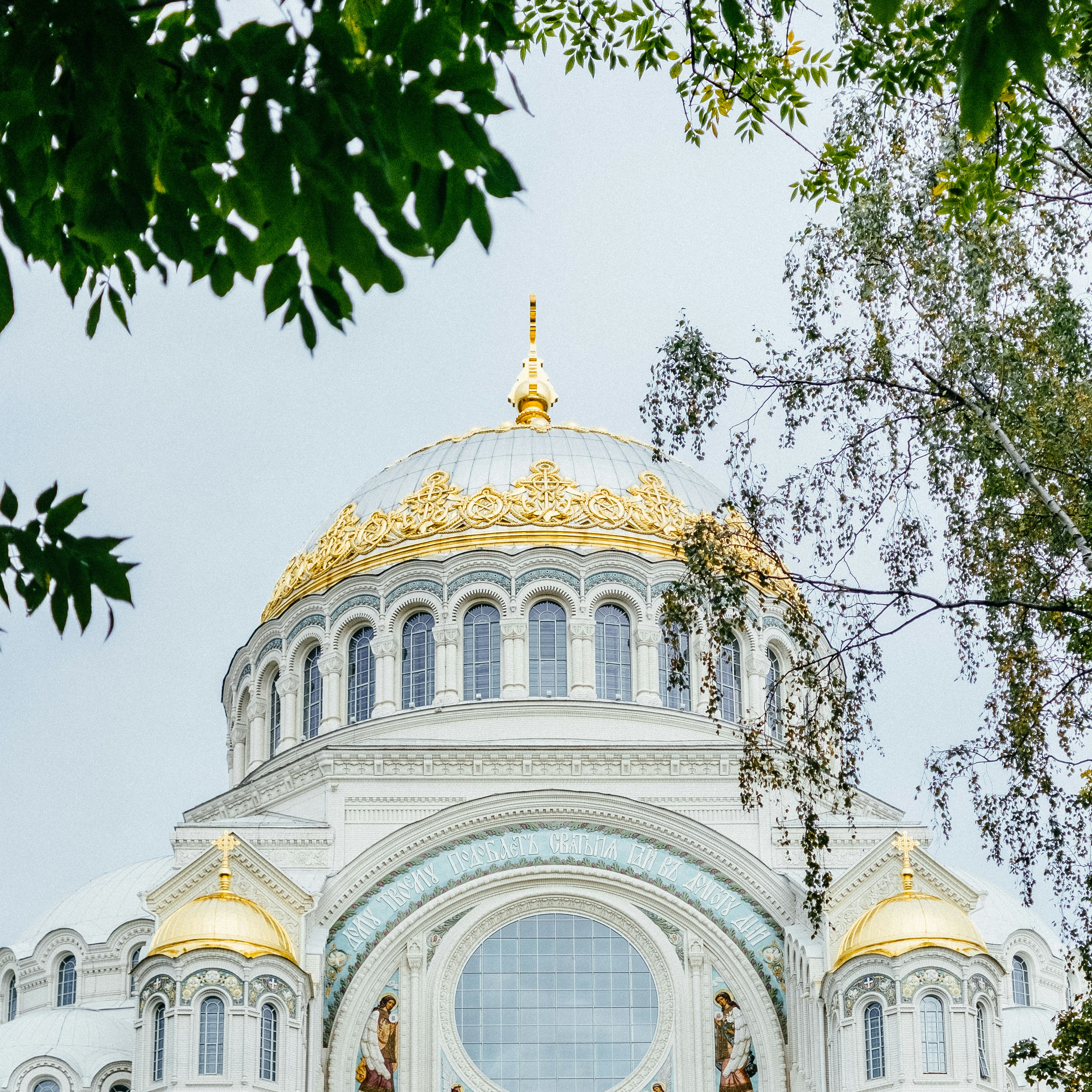 Ornate dome with golden accents and large windows framed by lush greenery. The architectural details reflect a blend of grandeur and serenity.