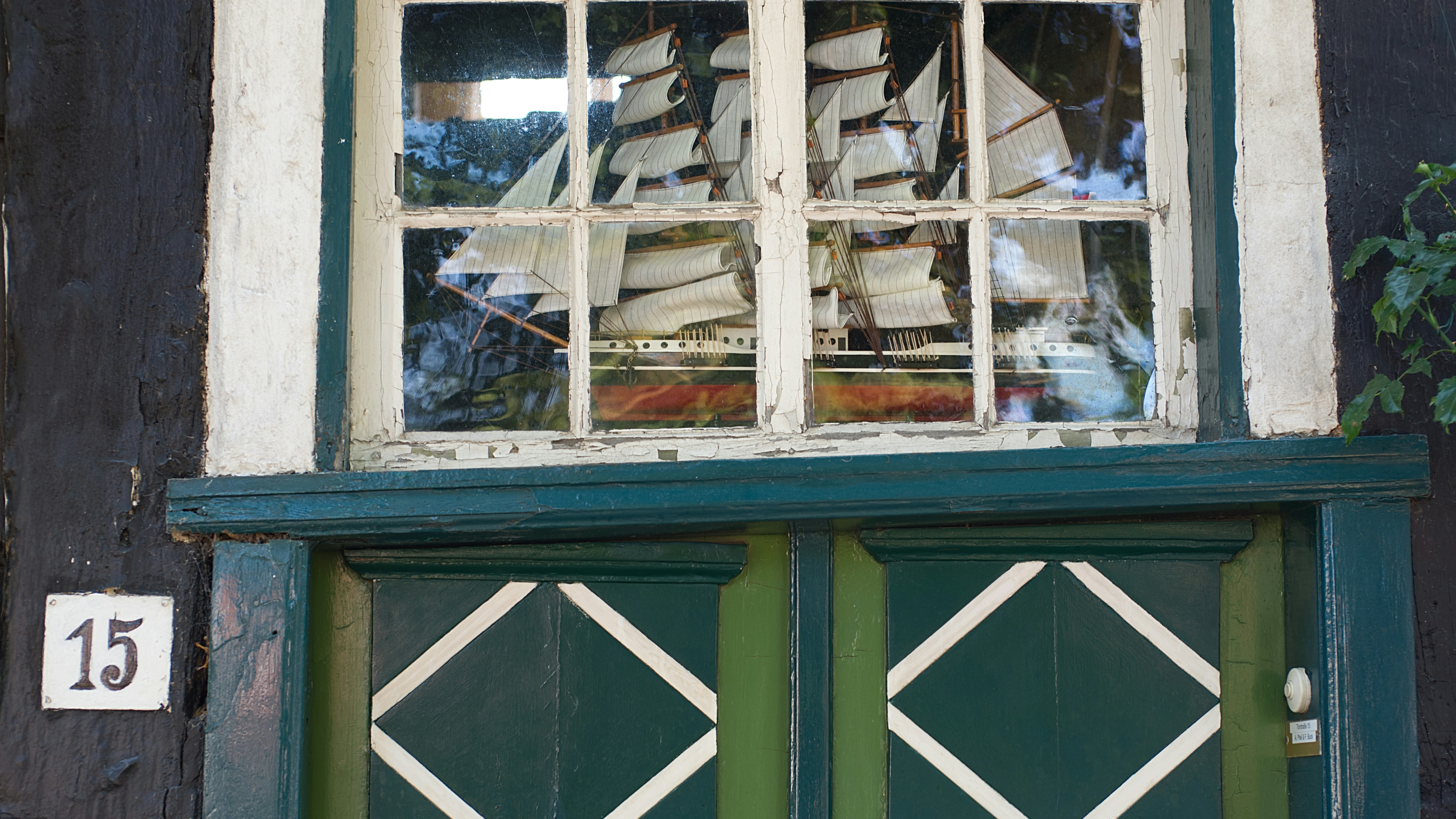 Model ship displayed behind a vintage green and white window, reflecting the surrounding trees.