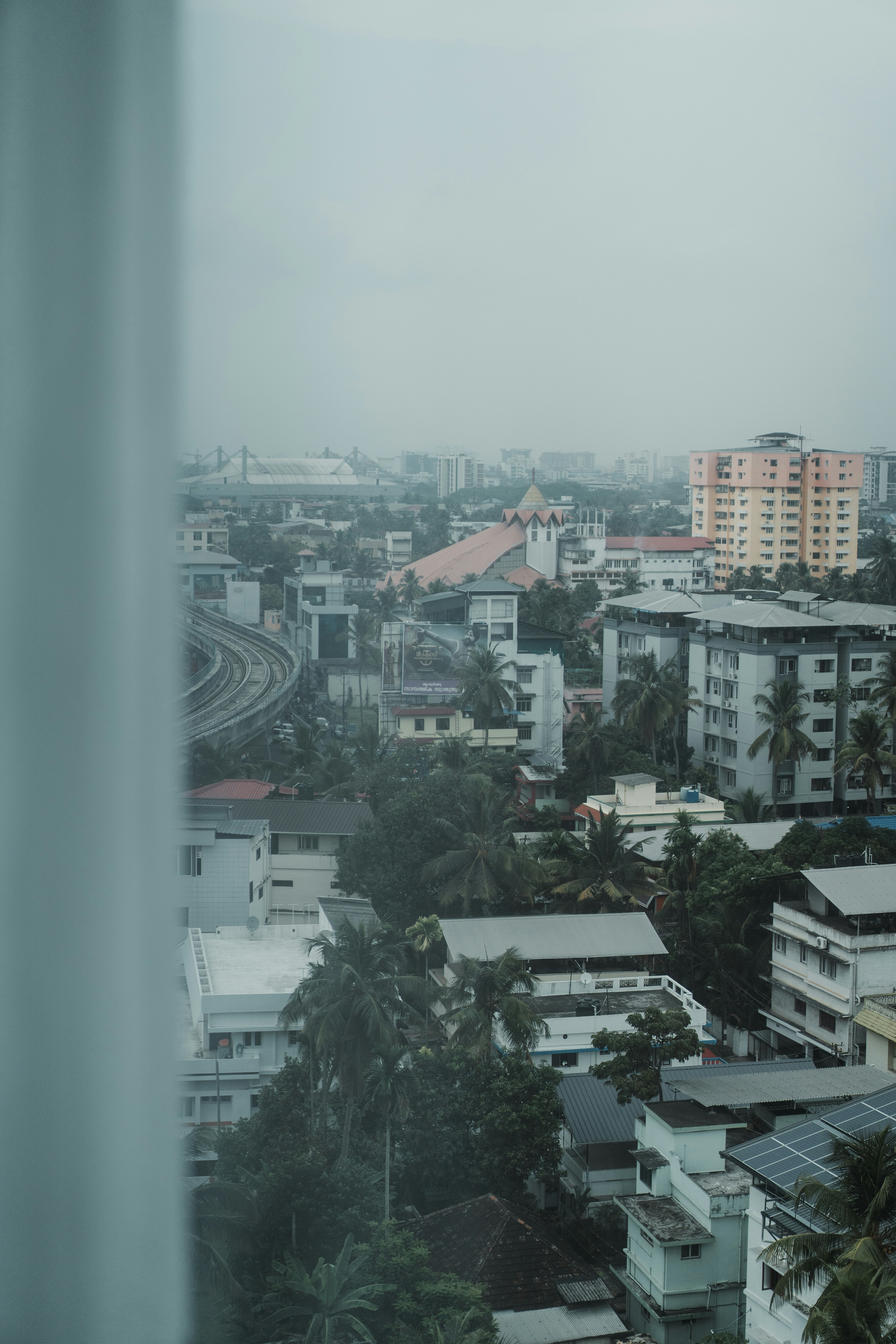 Cityscape with colorful buildings and lush palm trees under a cloudy sky.