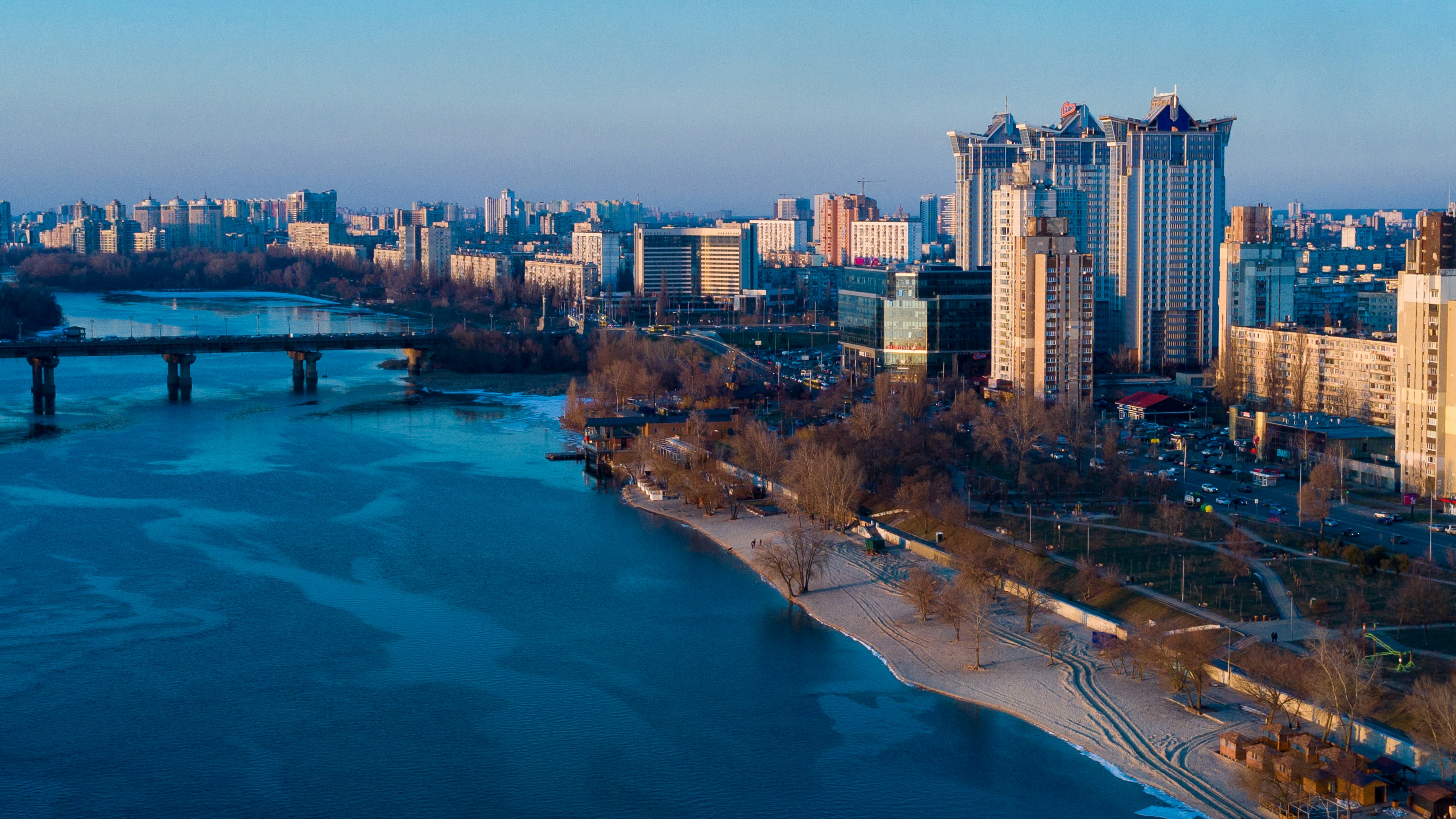 Aerial view of a cityscape along a river, showcasing modern architecture and a tranquil shoreline. The scene captures the harmonious blend of nature and urban life.