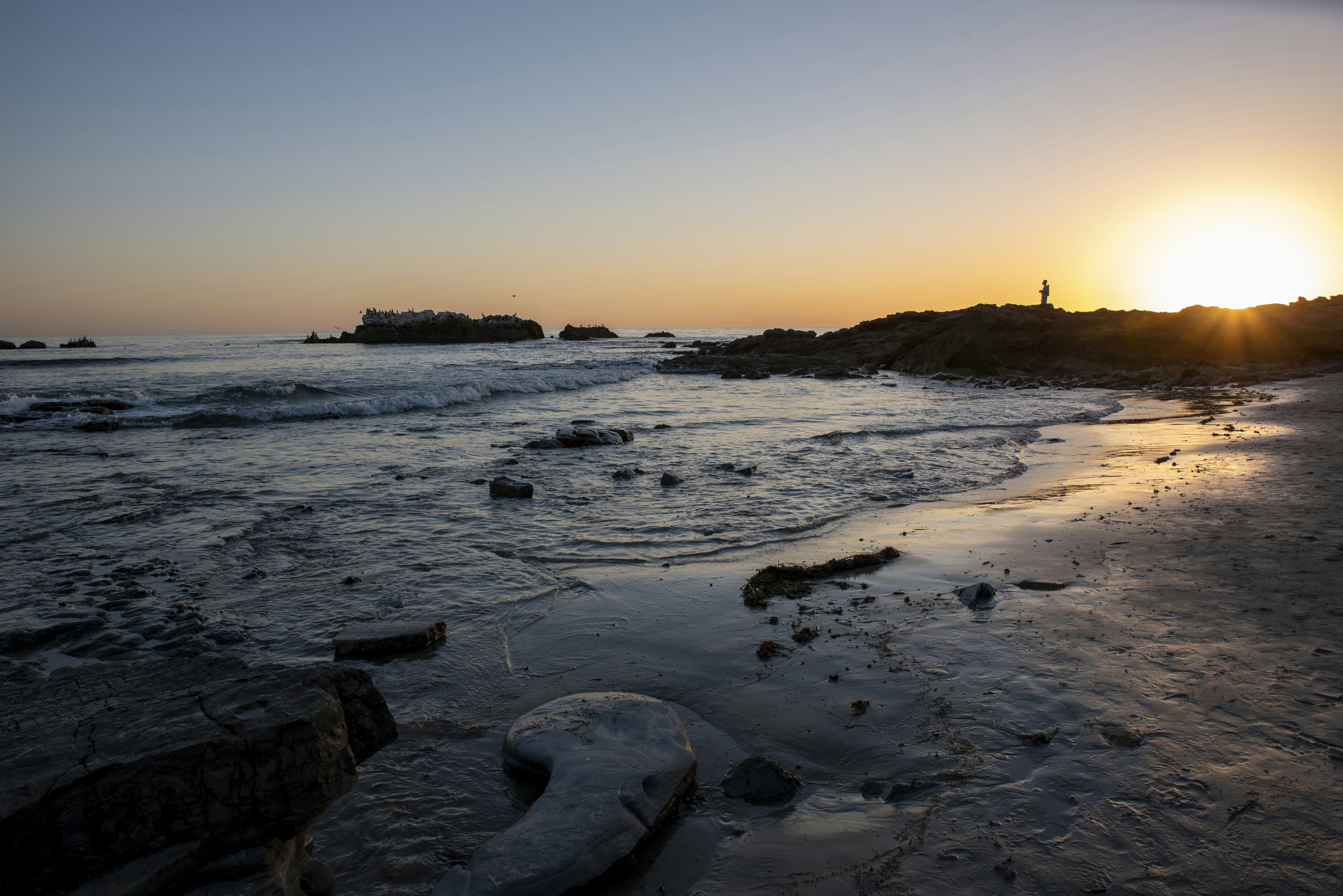 Silhouette of person standing on rock formation on sea shore during ...