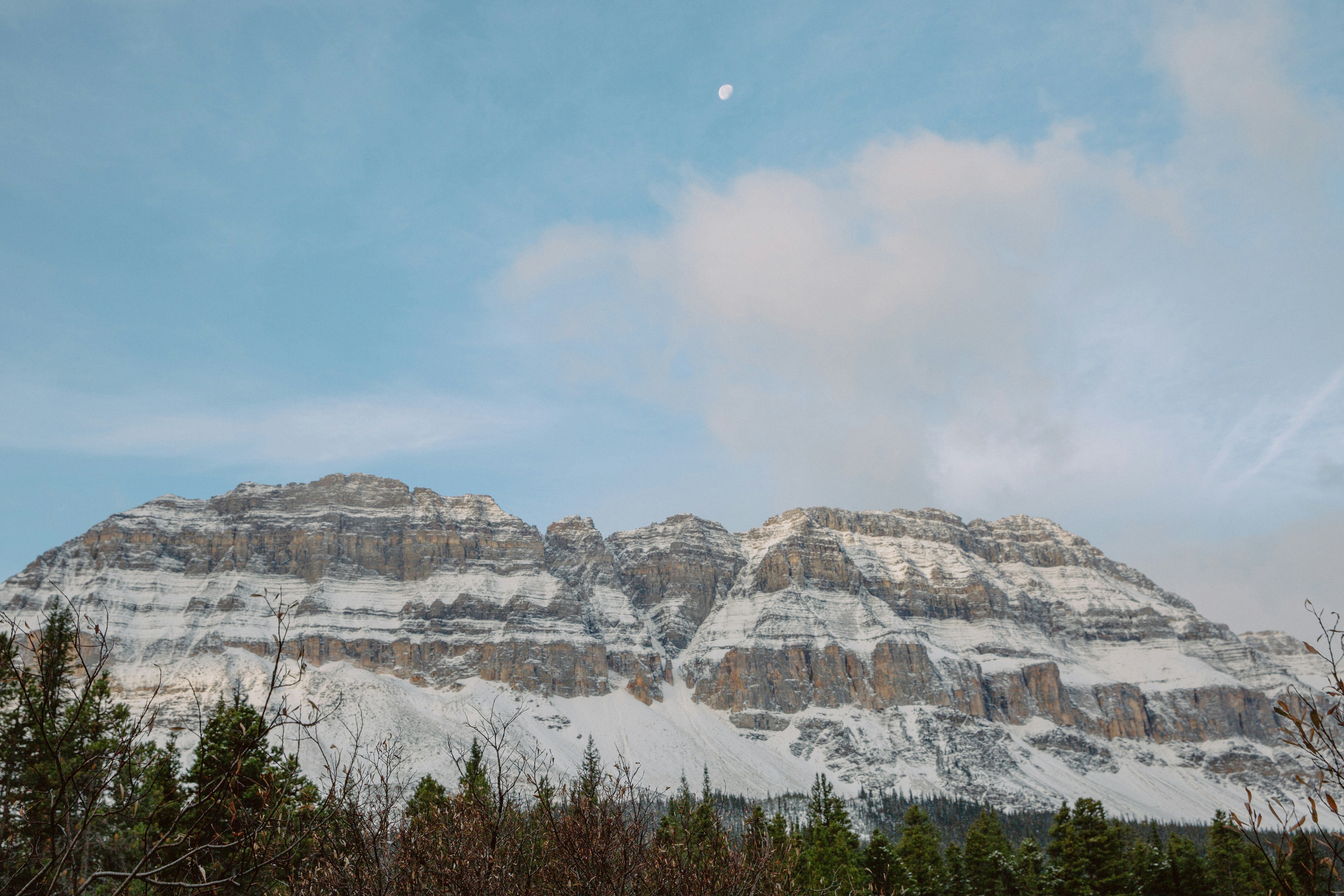 Snow-covered mountain range under a clear sky, with a hint of moonlight illuminating the scene.