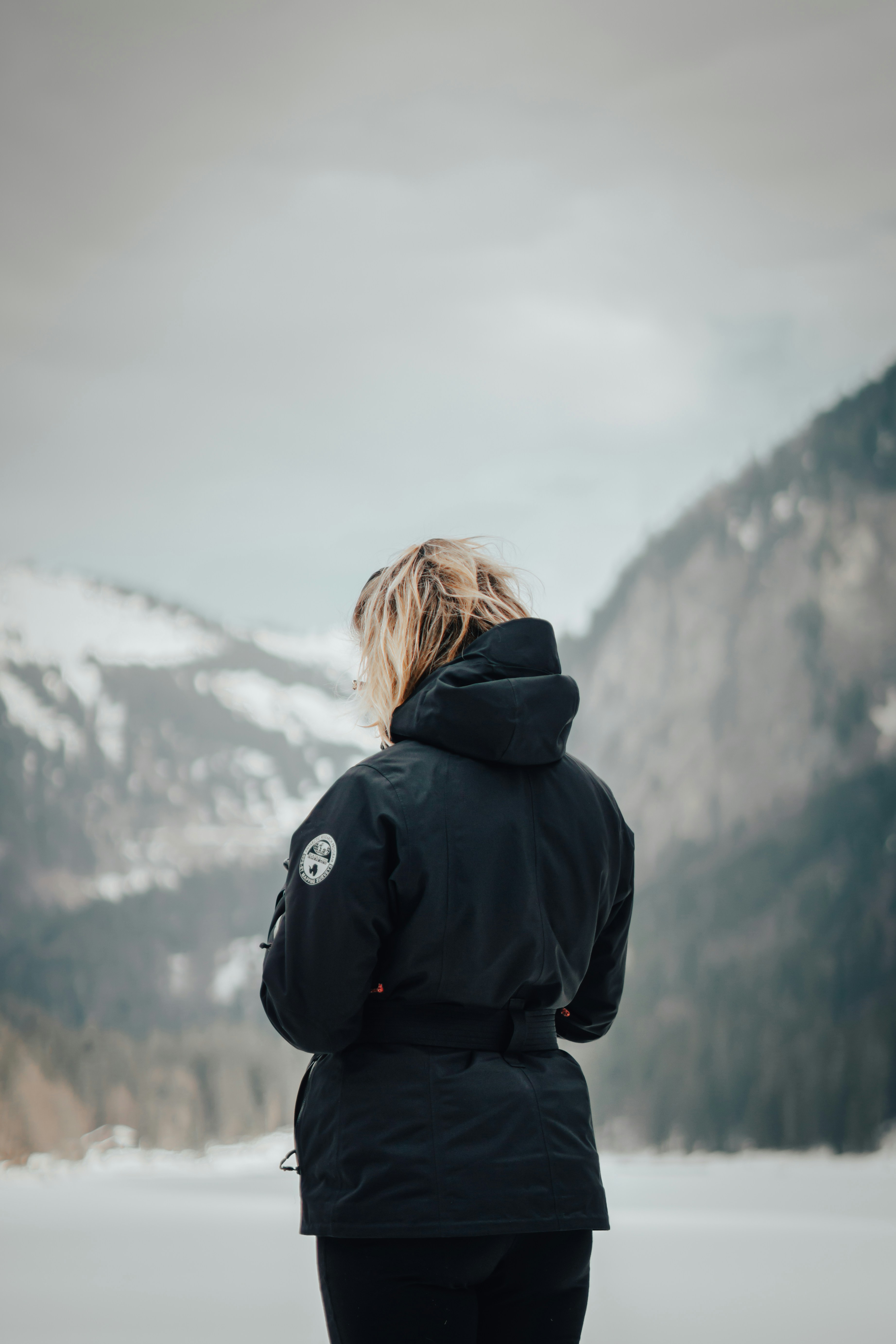 A person stands with their back to the camera, gazing at a serene snowy landscape with mountains in the background. The scene evokes a sense of contemplation and connection with nature.