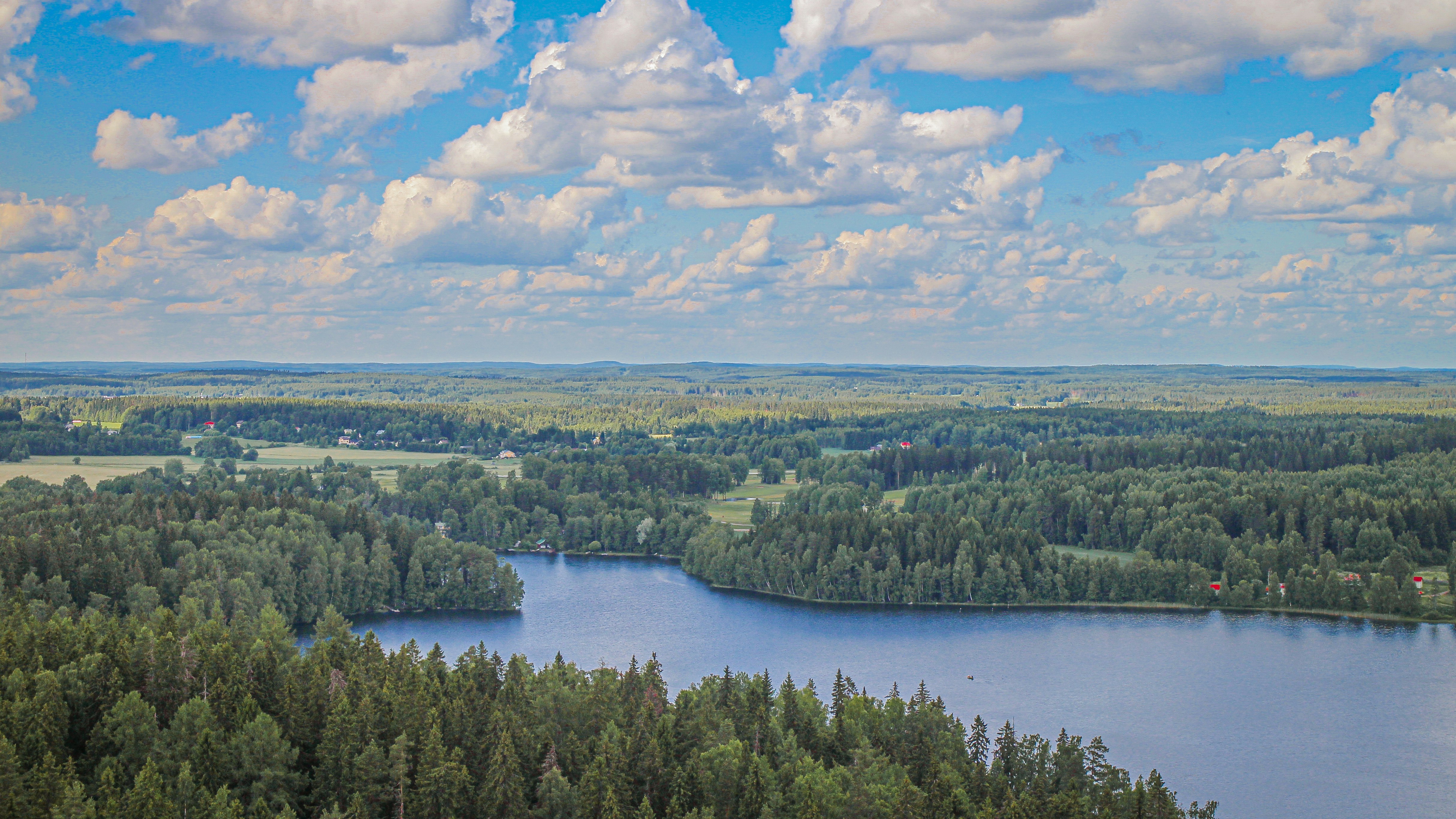 Expansive view of a Finnish forest surrounding a serene lake under a sky dotted with clouds.